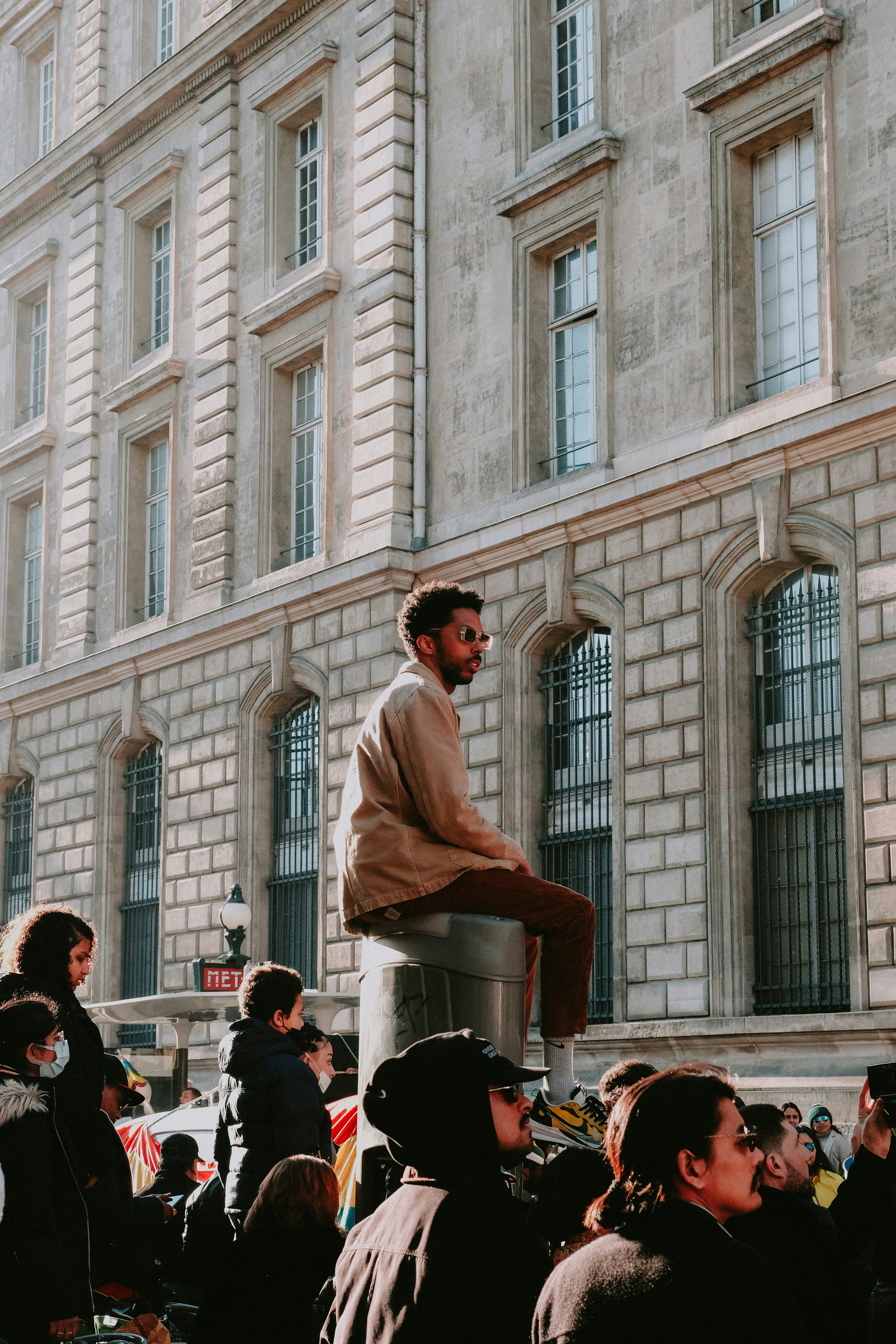A man sitting on top of a bucket in front of a crowd of people photo ...