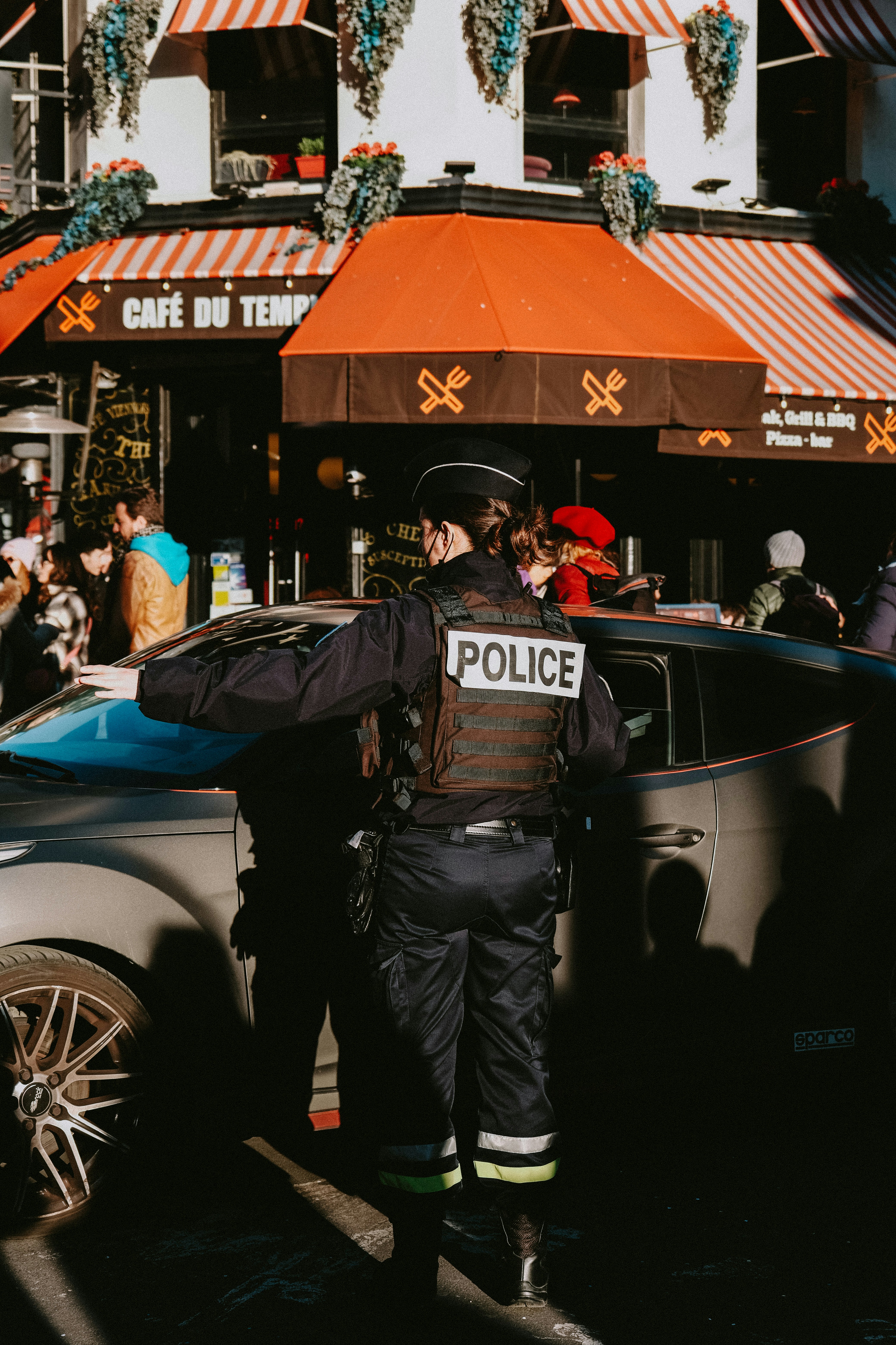 Café Frontline: A Police Officer Stands Guard by a Car on a Busy Street