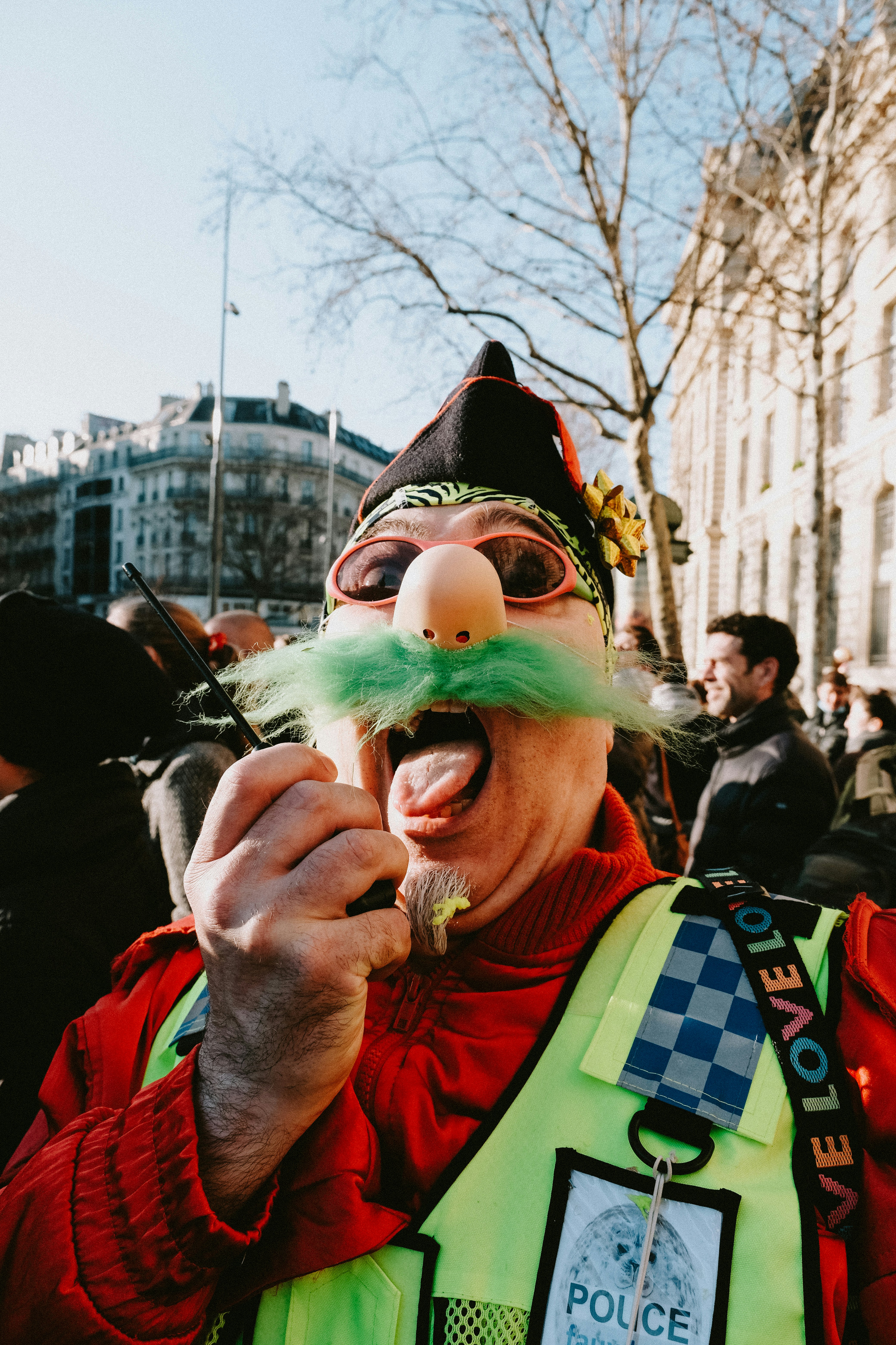 A vibrant protester sporting a colorful costume, oversized nose, and green mustache, joyfully engaging with the crowd. The scene captures the spirit of activism infused with humor.