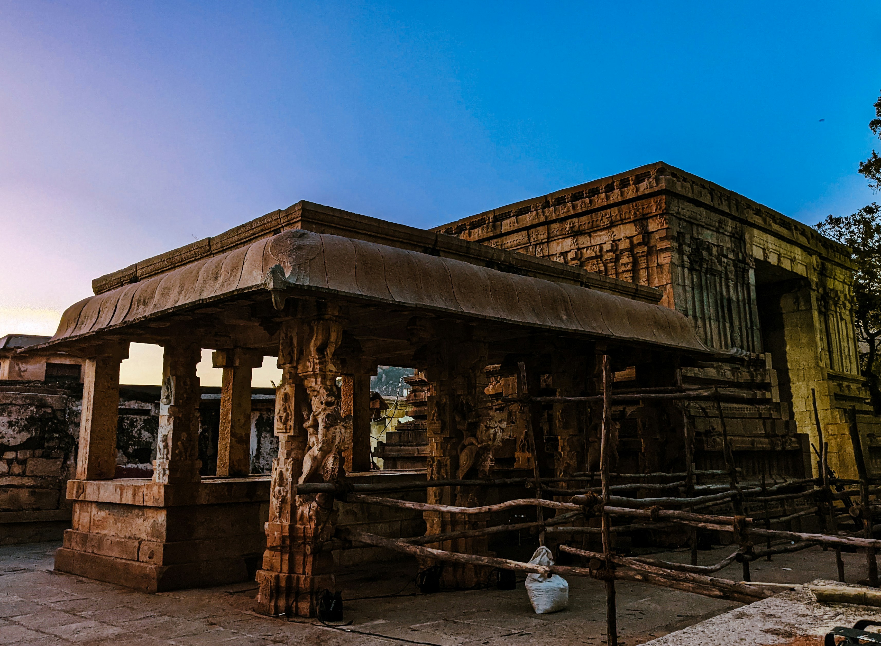 Ancient stone pavilion with carved columns under a fabric canopy, bathed in warm sunset tones.