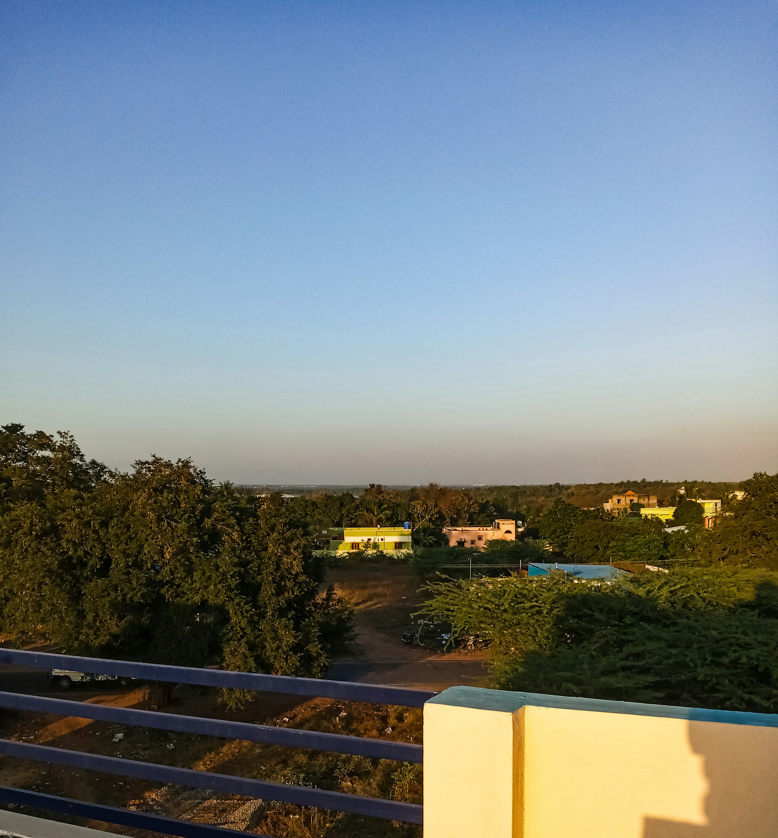 A panoramic view of a tranquil suburban landscape, featuring lush greenery and scattered houses under a clear blue sky.
