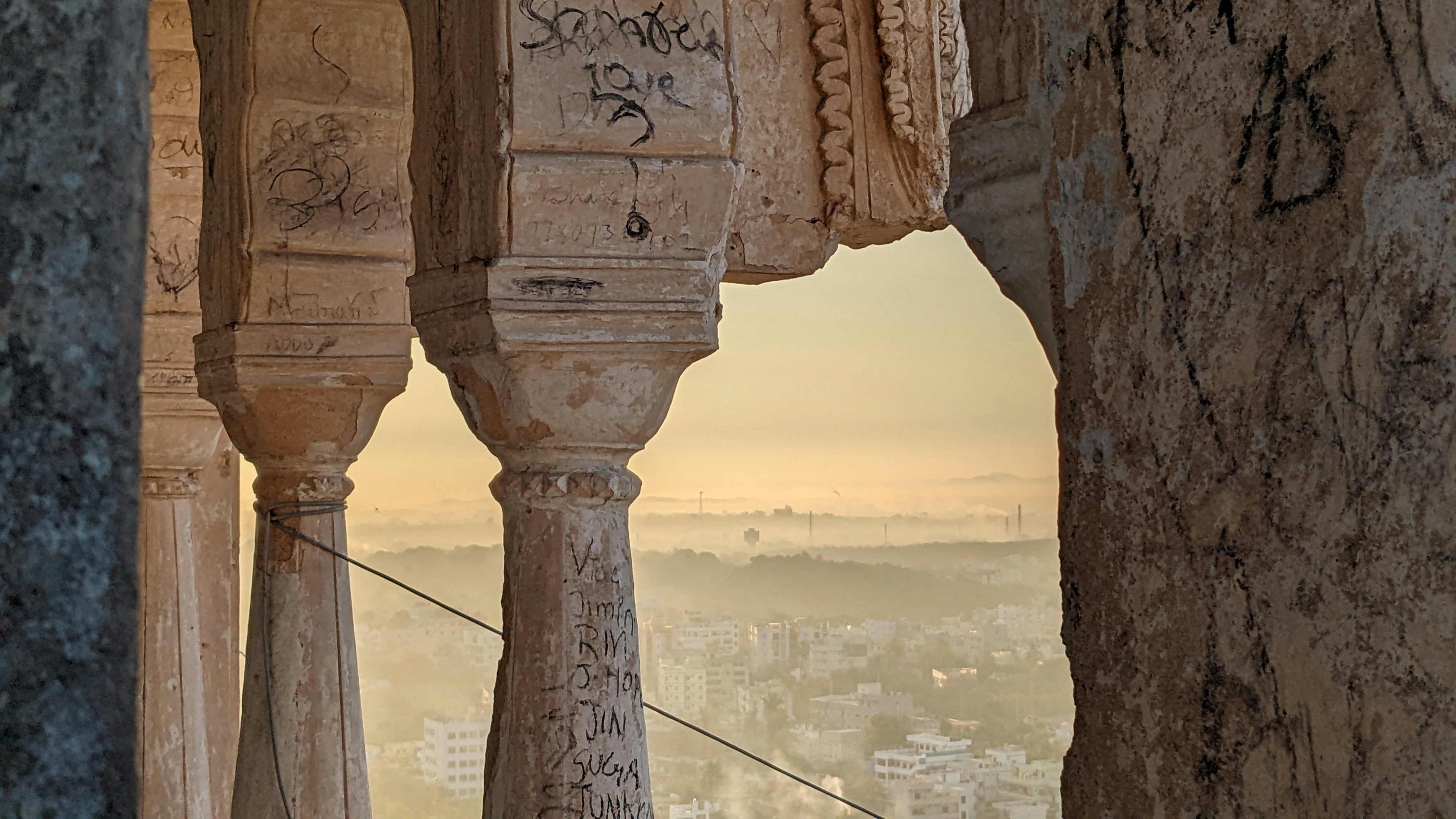 Stone pillars and arches overlook a misty cityscape at dawn.