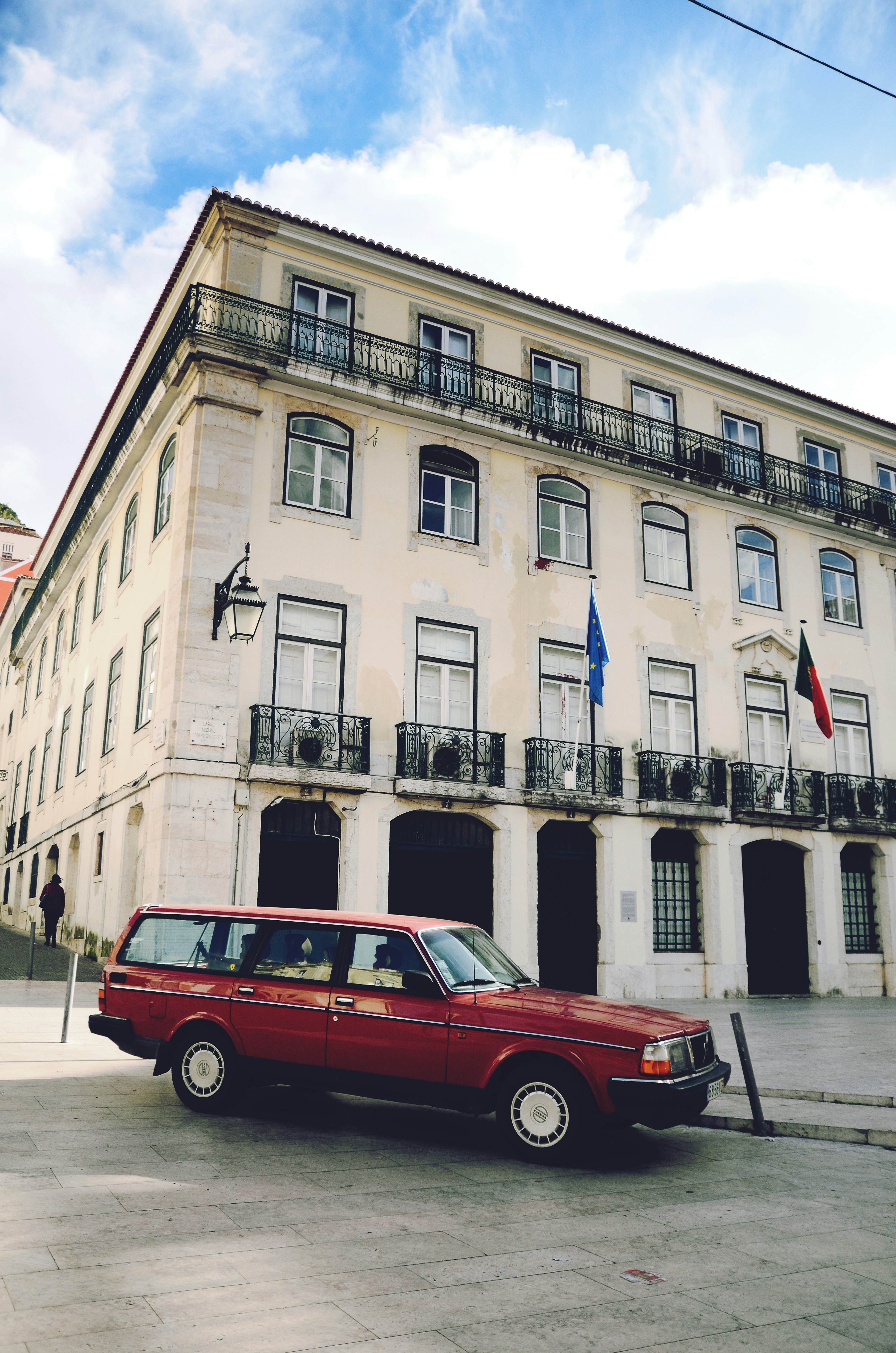 Red Vintage Wagon Anchors a European Facade Under Flags