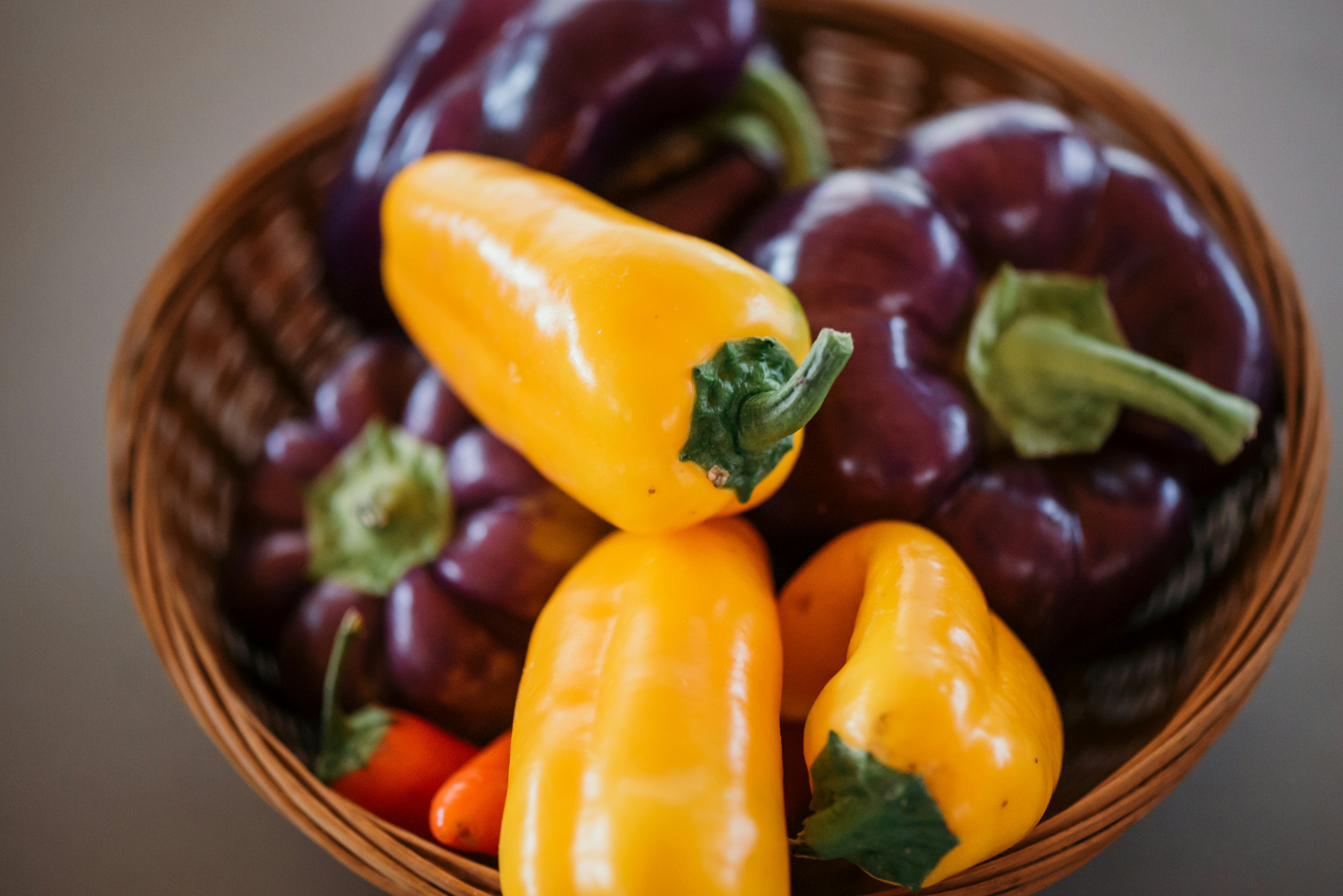 Colorful assortment of bell peppers and chili peppers arranged in a woven basket, showcasing their fresh and vibrant hues.