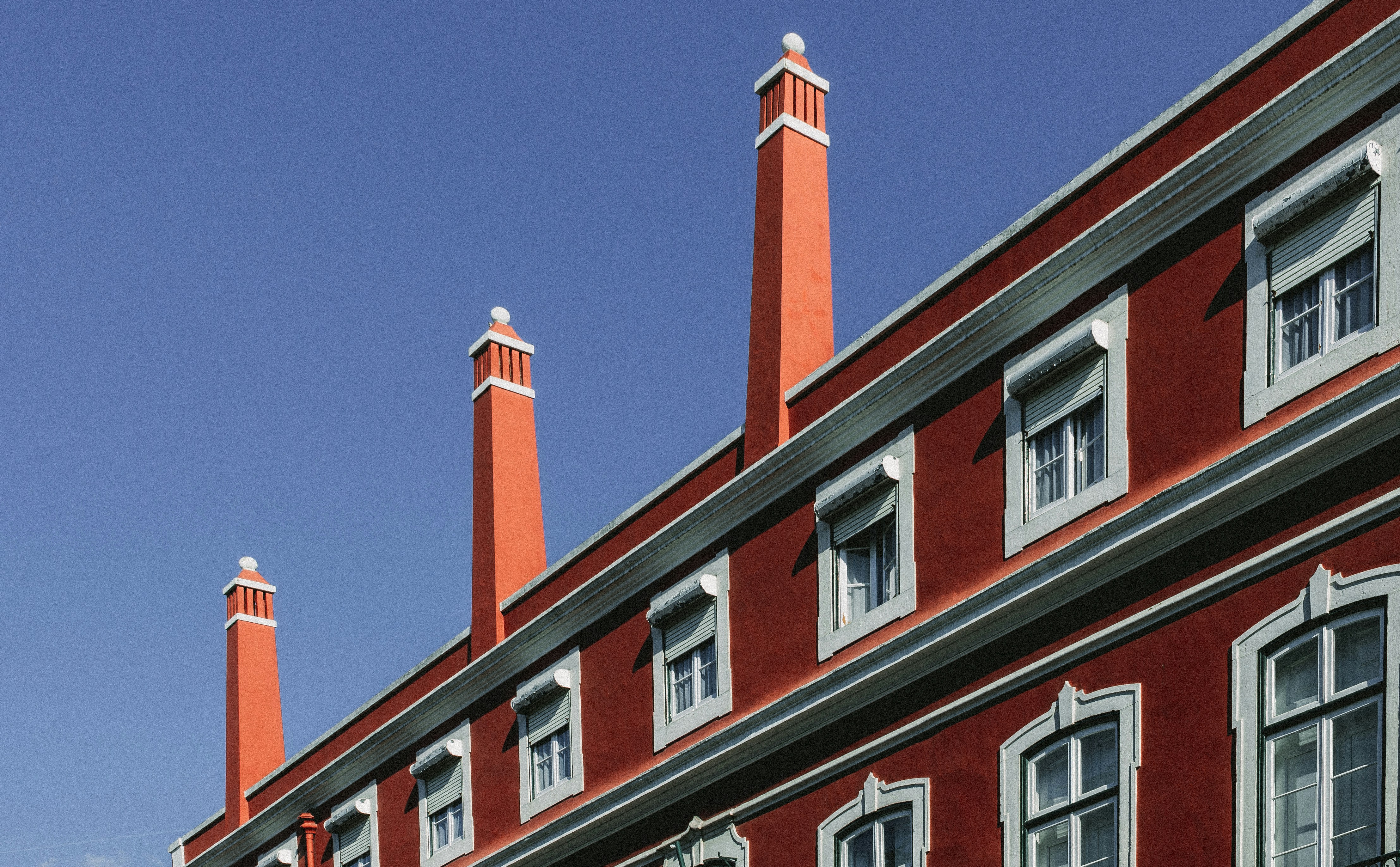 A striking red building featuring distinct chimneys and ornate window details against a clear blue sky.