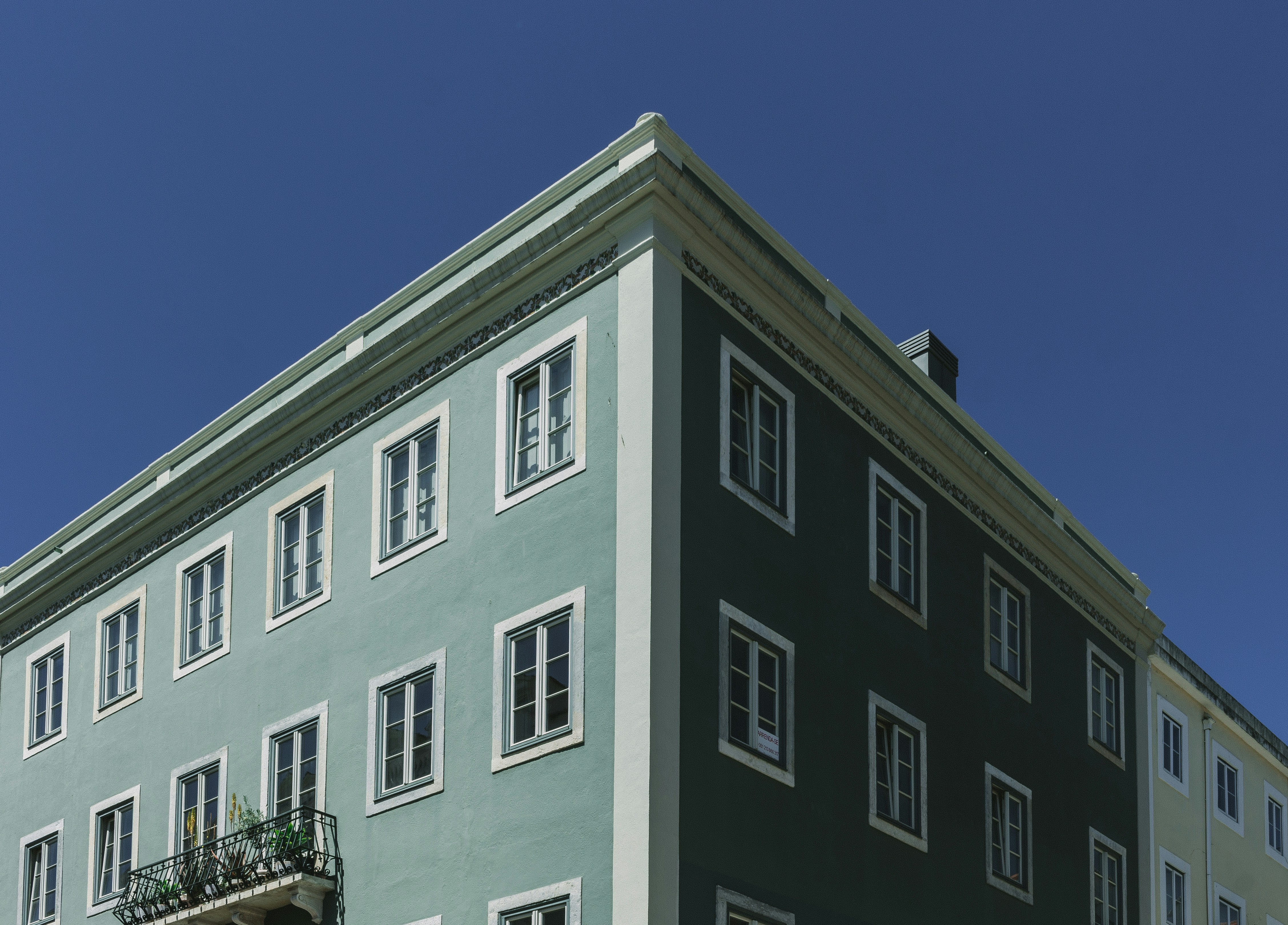 Teal Corner Facade: Sunlit Geometry Against a Clear Sky