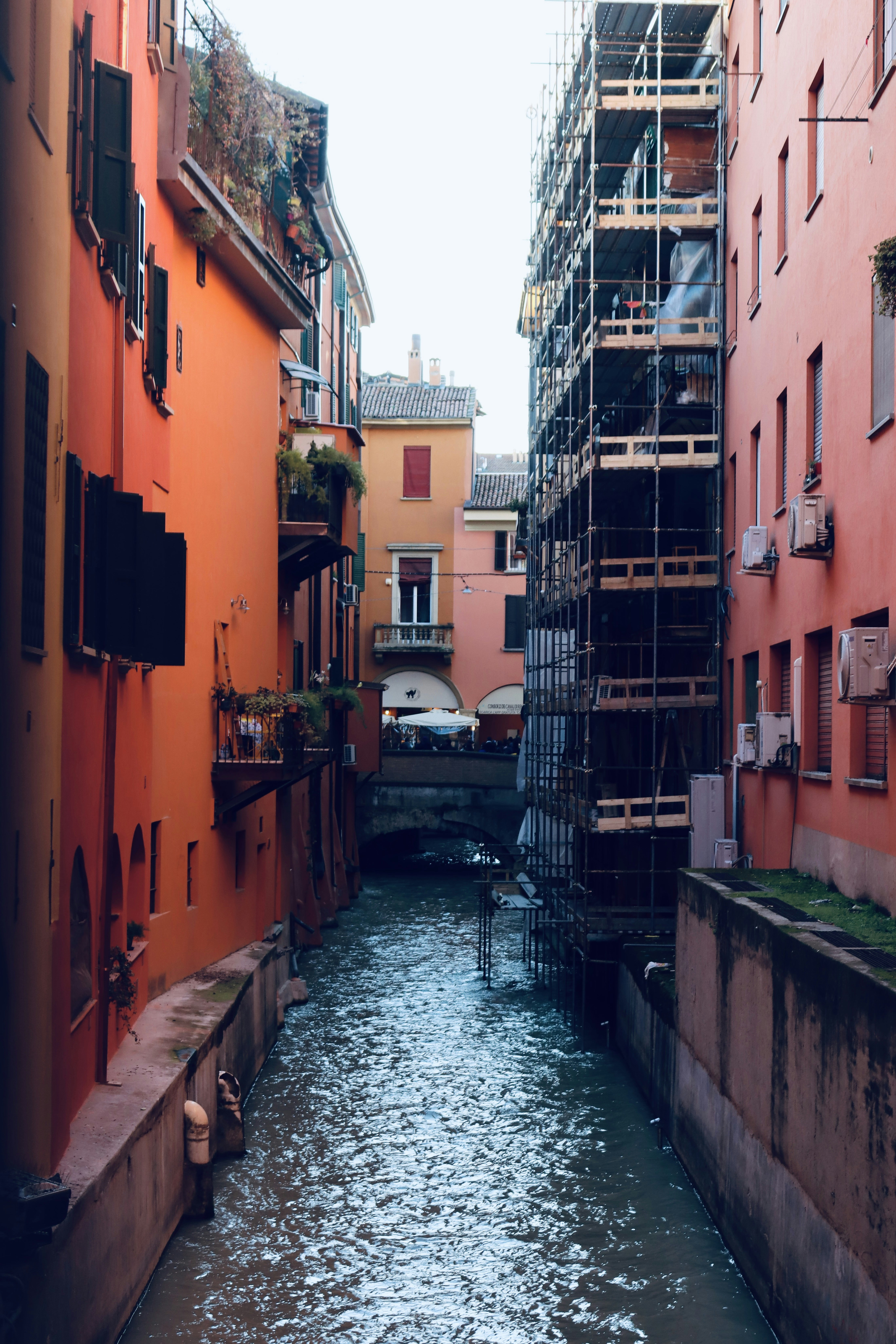 Narrow canal flanked by vibrant buildings, with scaffolding hinting at ongoing renovations. Water reflects the colorful facades above.