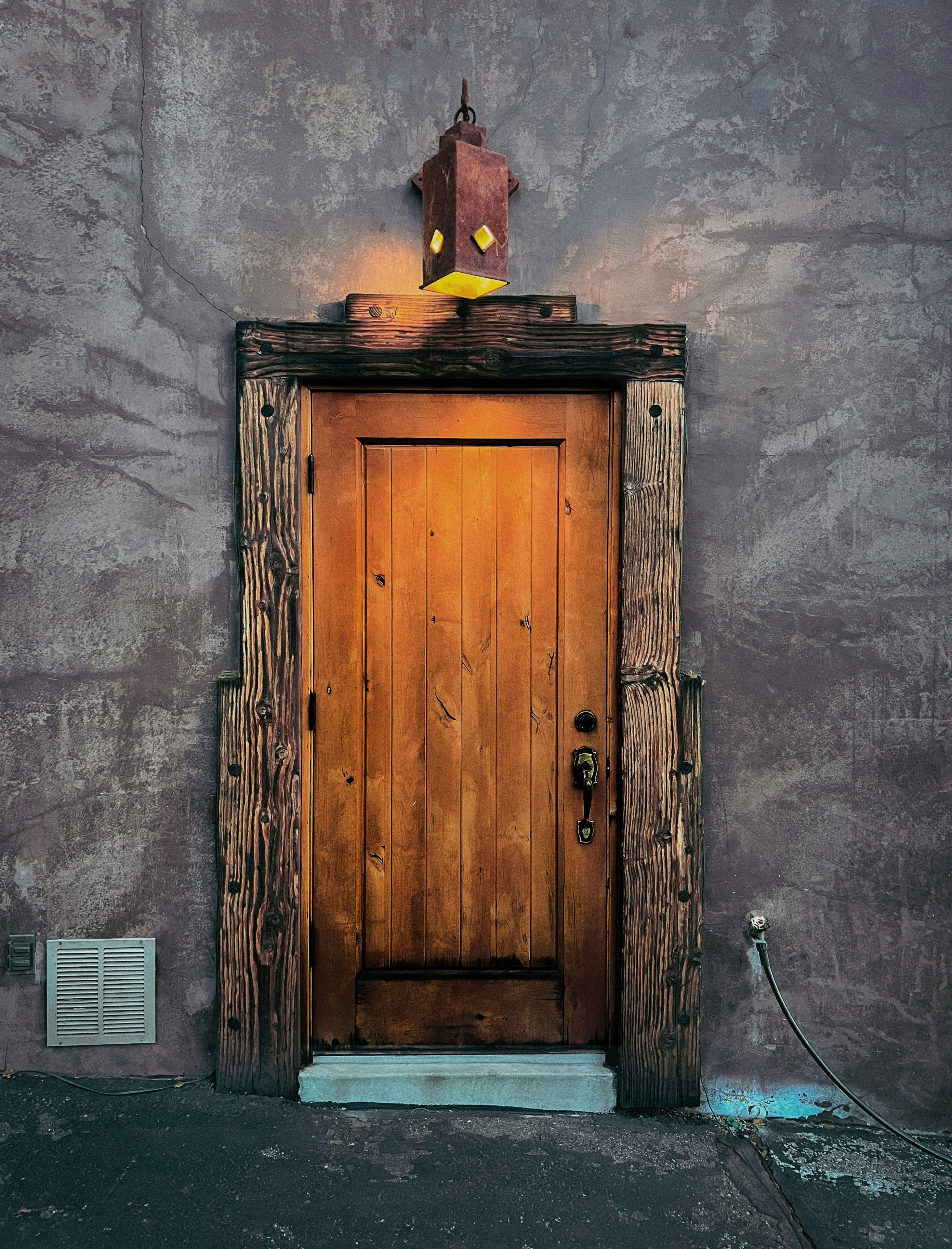 Lantern-Lit Portal: Weathered Doorway Framed by Rough Timber