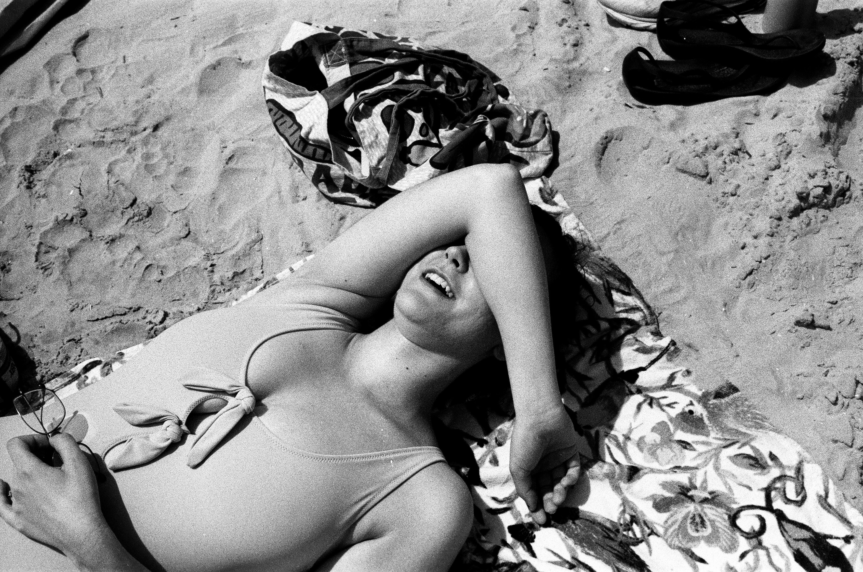 Woman reclining on a floral beach towel, playfully shielding her face from the sun. The sandy beach setting enhances the relaxed atmosphere.