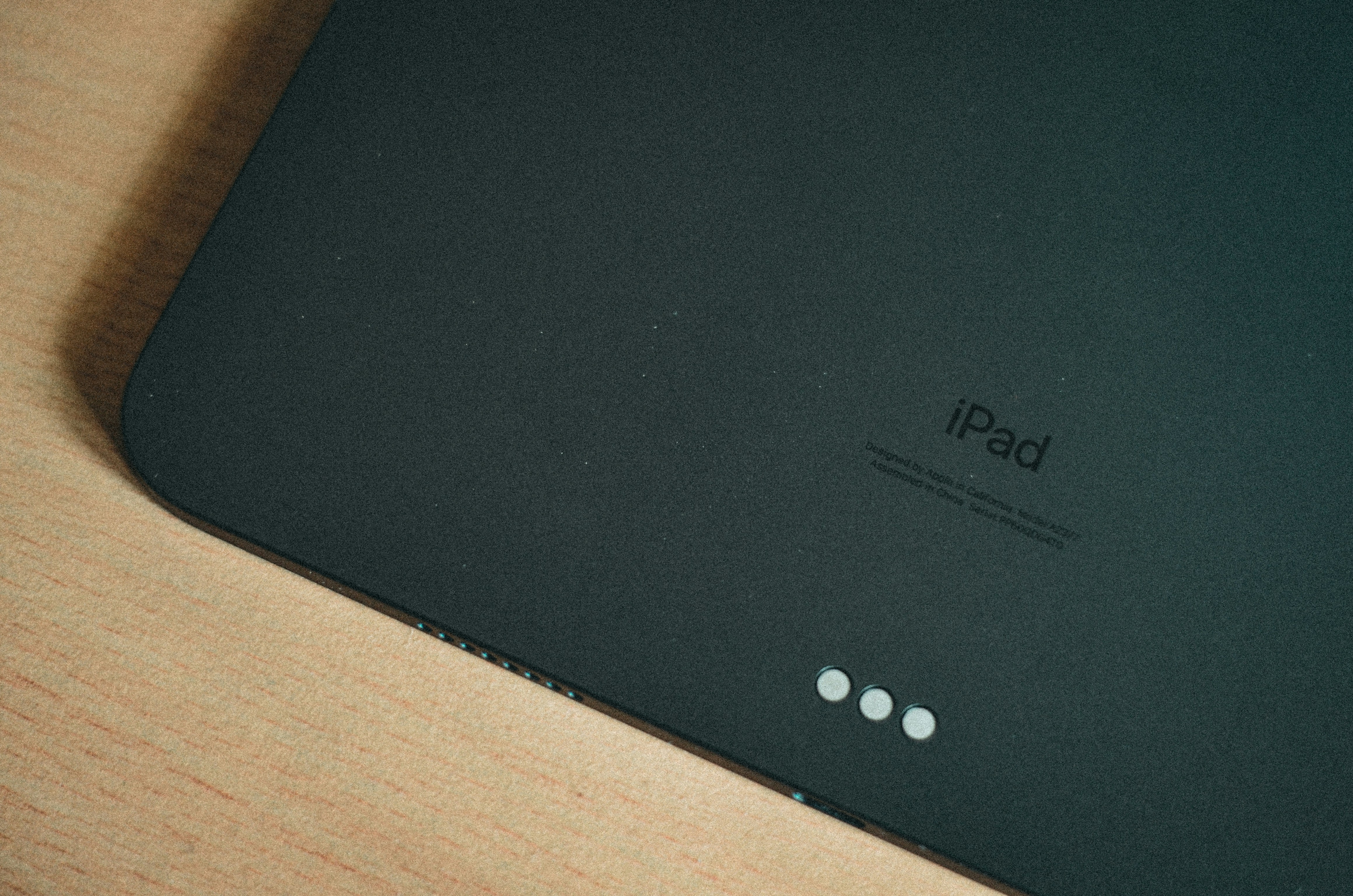 Close-up of a sleek black iPad resting on a wooden surface, showcasing its minimalist design and branding.