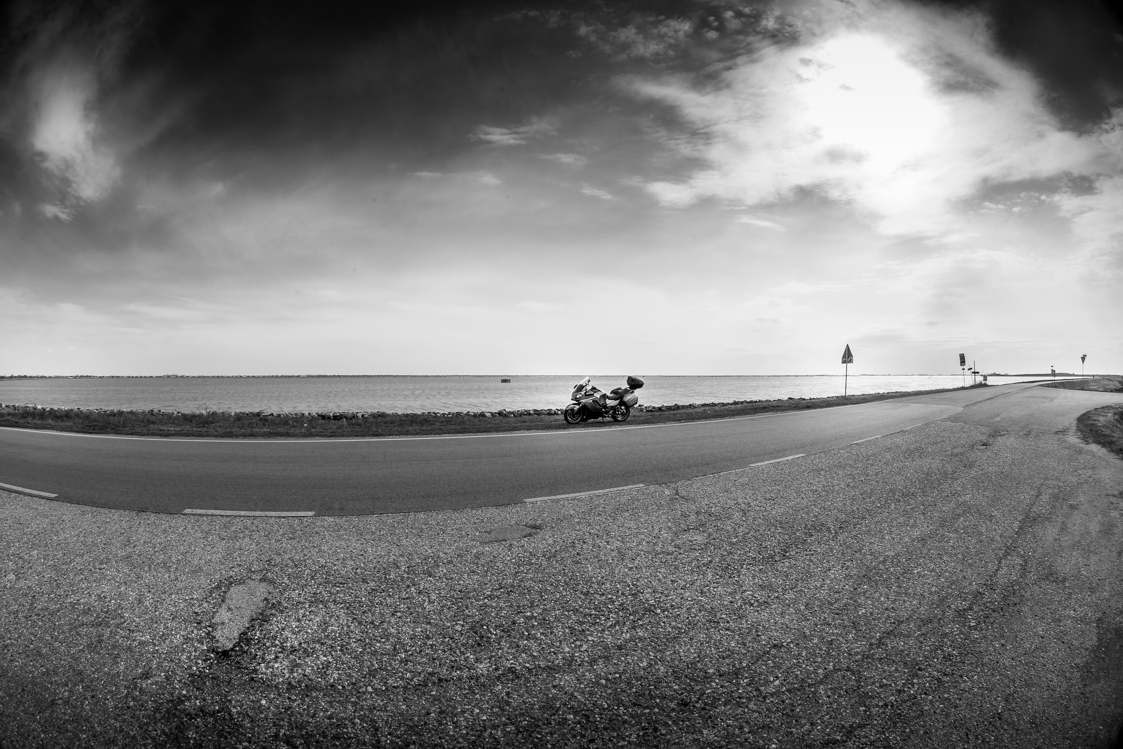 Motorcycle parked beside a curving coastal road under a dramatic sky.