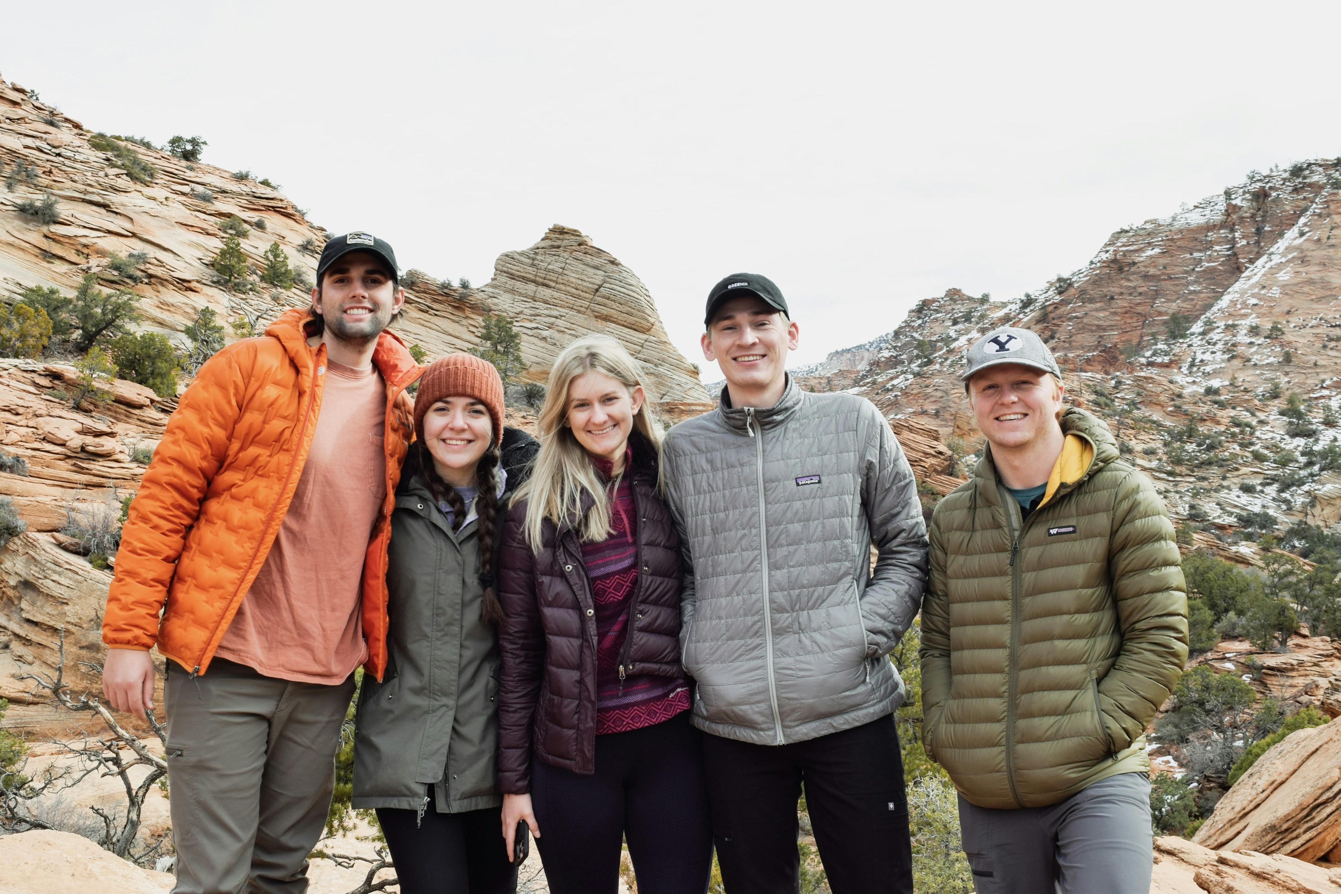 Group of five friends posing together in a rocky outdoor setting, showcasing their vibrant jackets against a natural backdrop. 