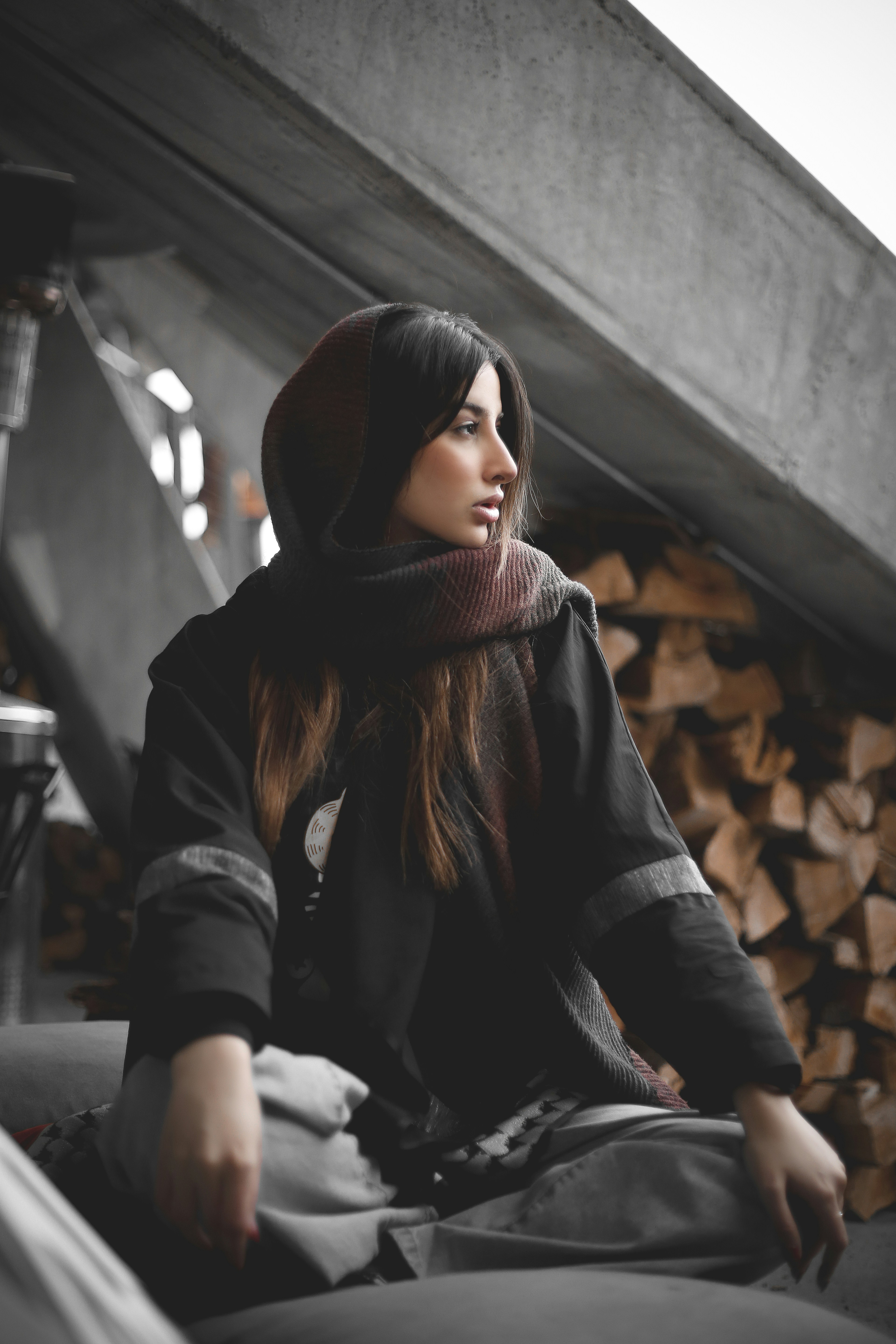 Hooded Quiet: Portrait in a Concrete Loft Among Stacked Firewood