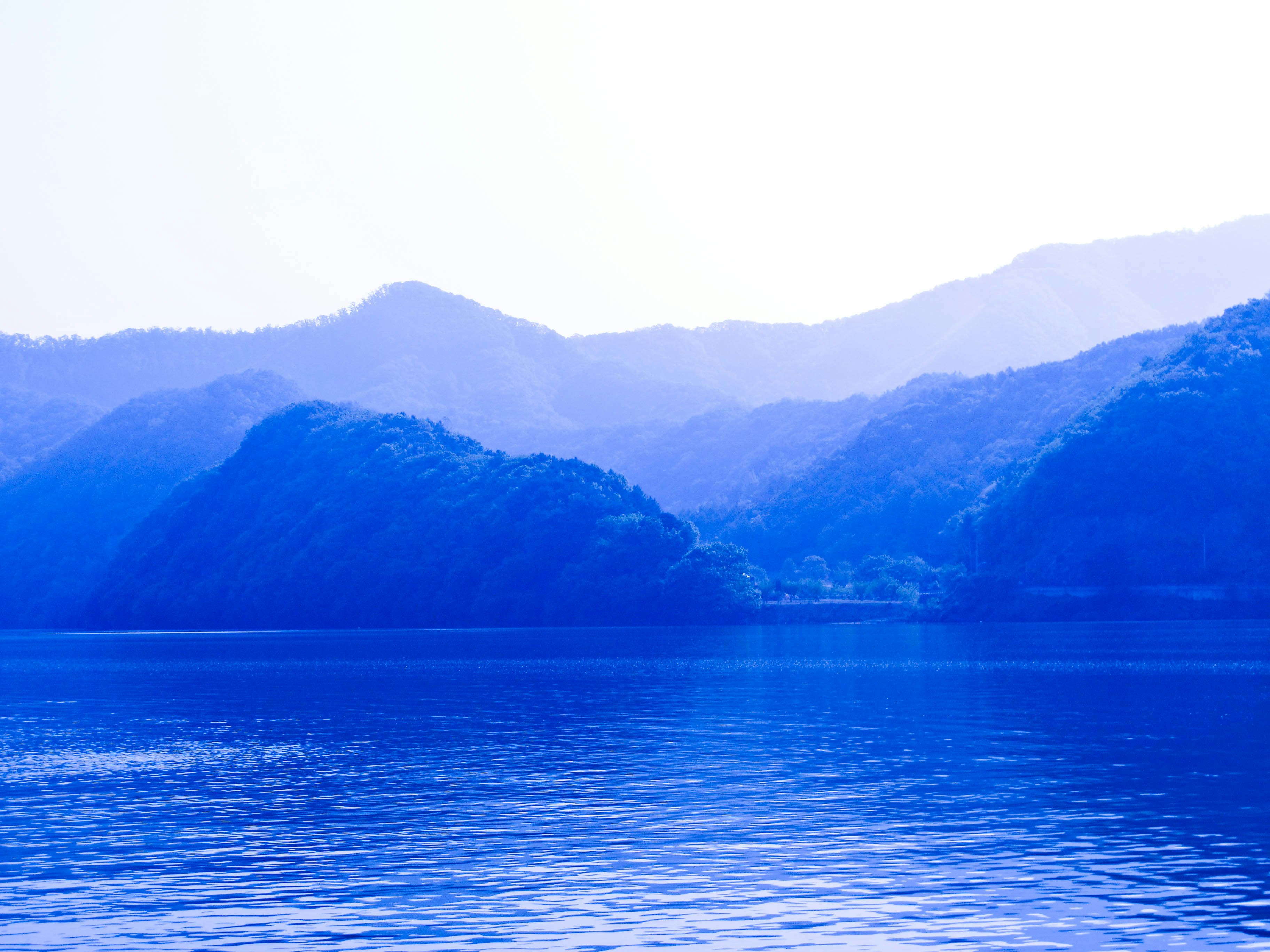 Serene landscape featuring layered blue mountains reflecting on calm waters under a soft light.