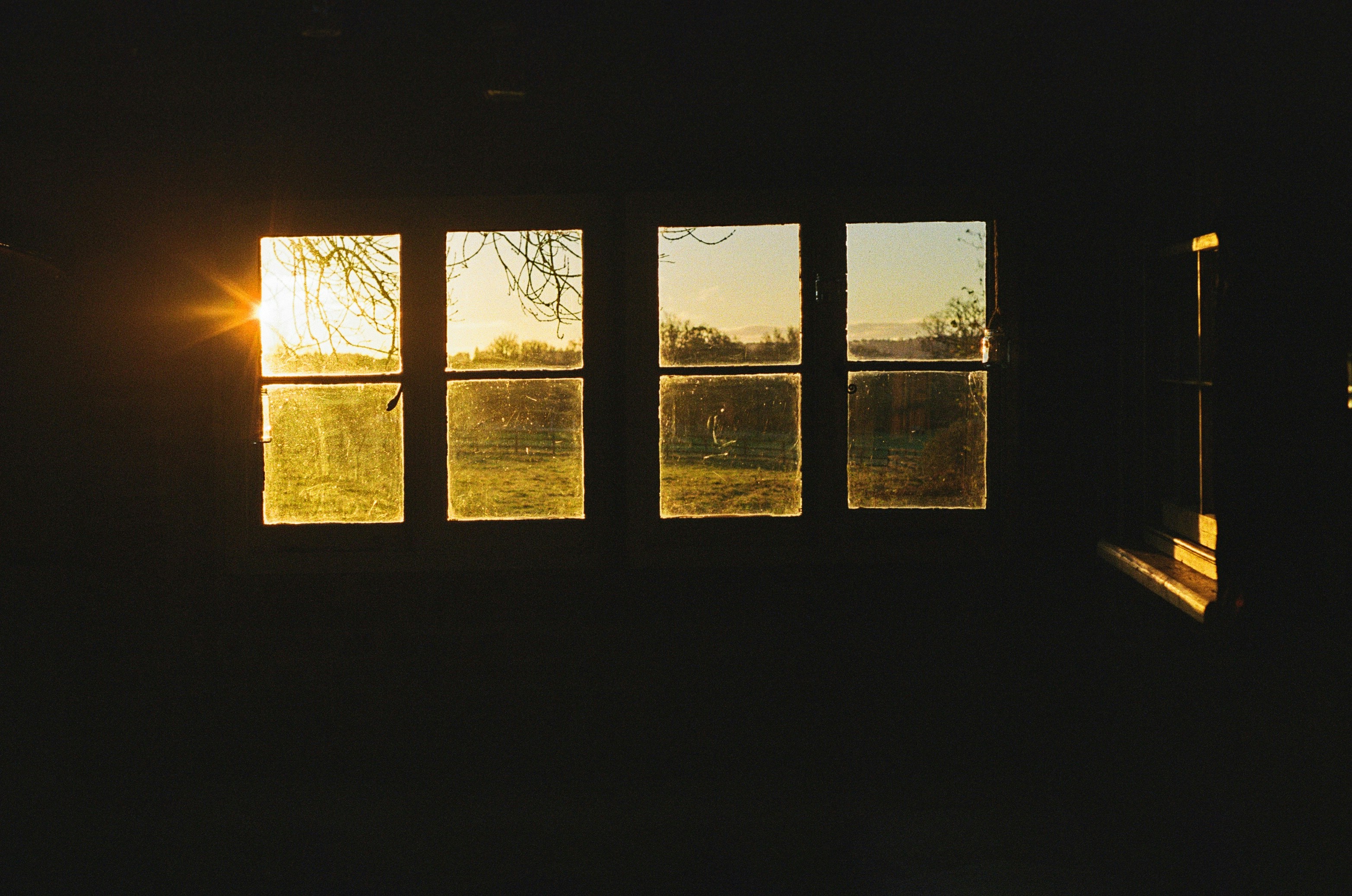 Sunrise illuminating a series of rustic windows, casting warm light into a darkened interior space.
