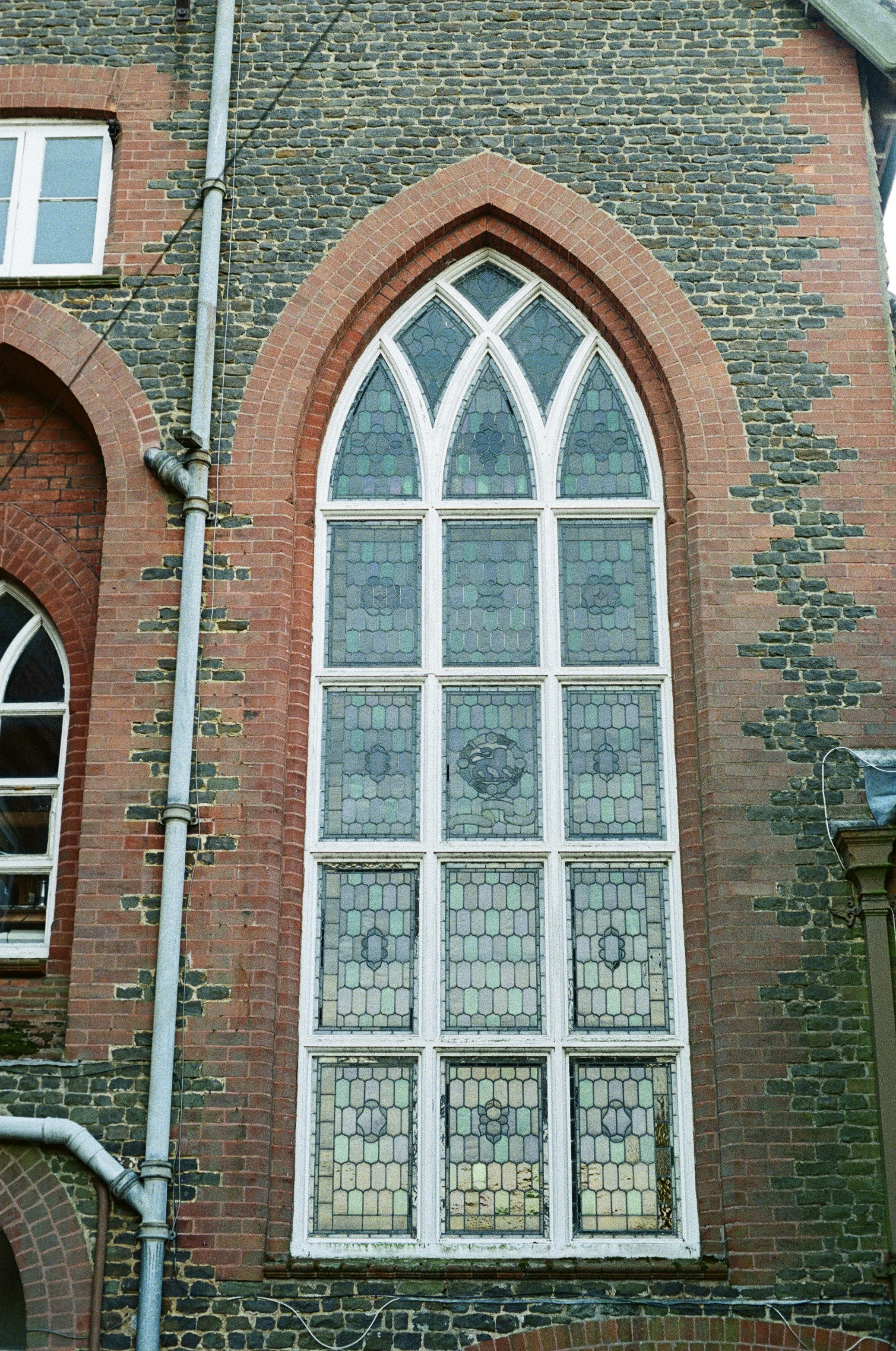Intricate stained glass window set in a brick wall, showcasing geometric patterns and historical craftsmanship.