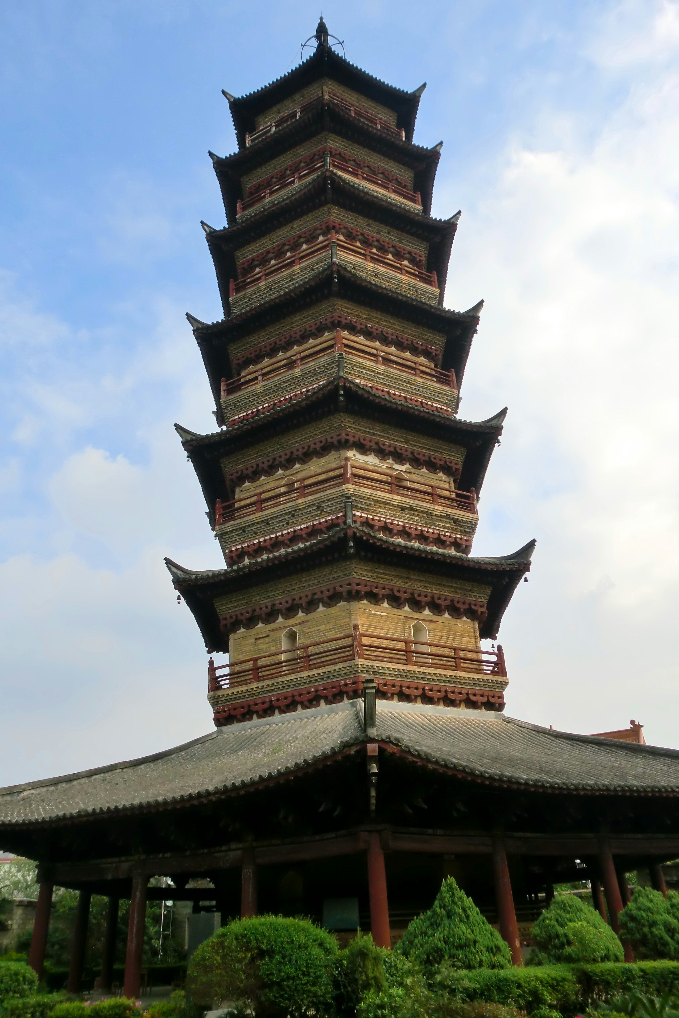 A traditional pagoda with intricate layers and ornate details, surrounded by lush greenery and a cloudy sky.