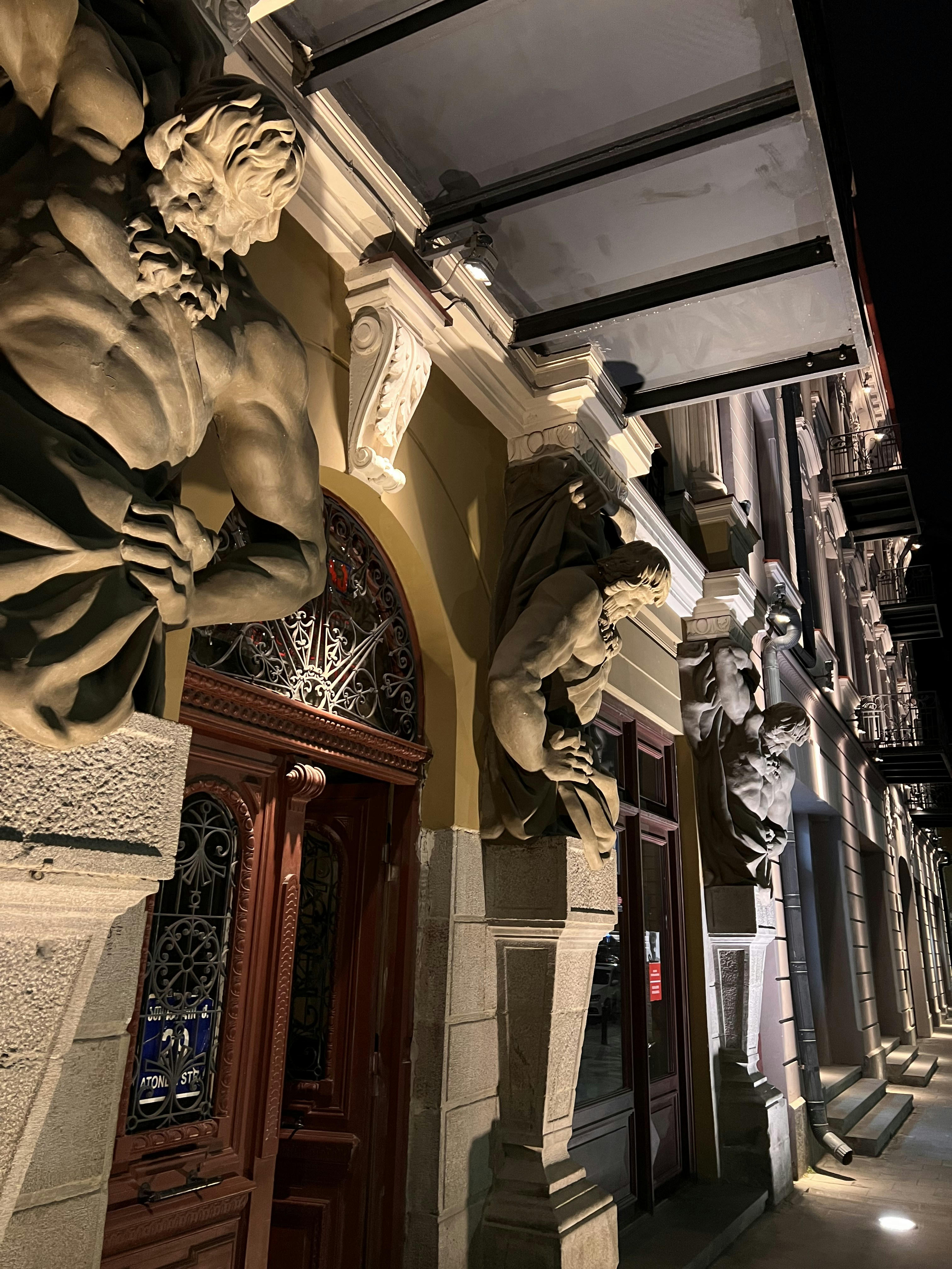 Stone Guardians Under Warm Nightlight Along a Classical Facade