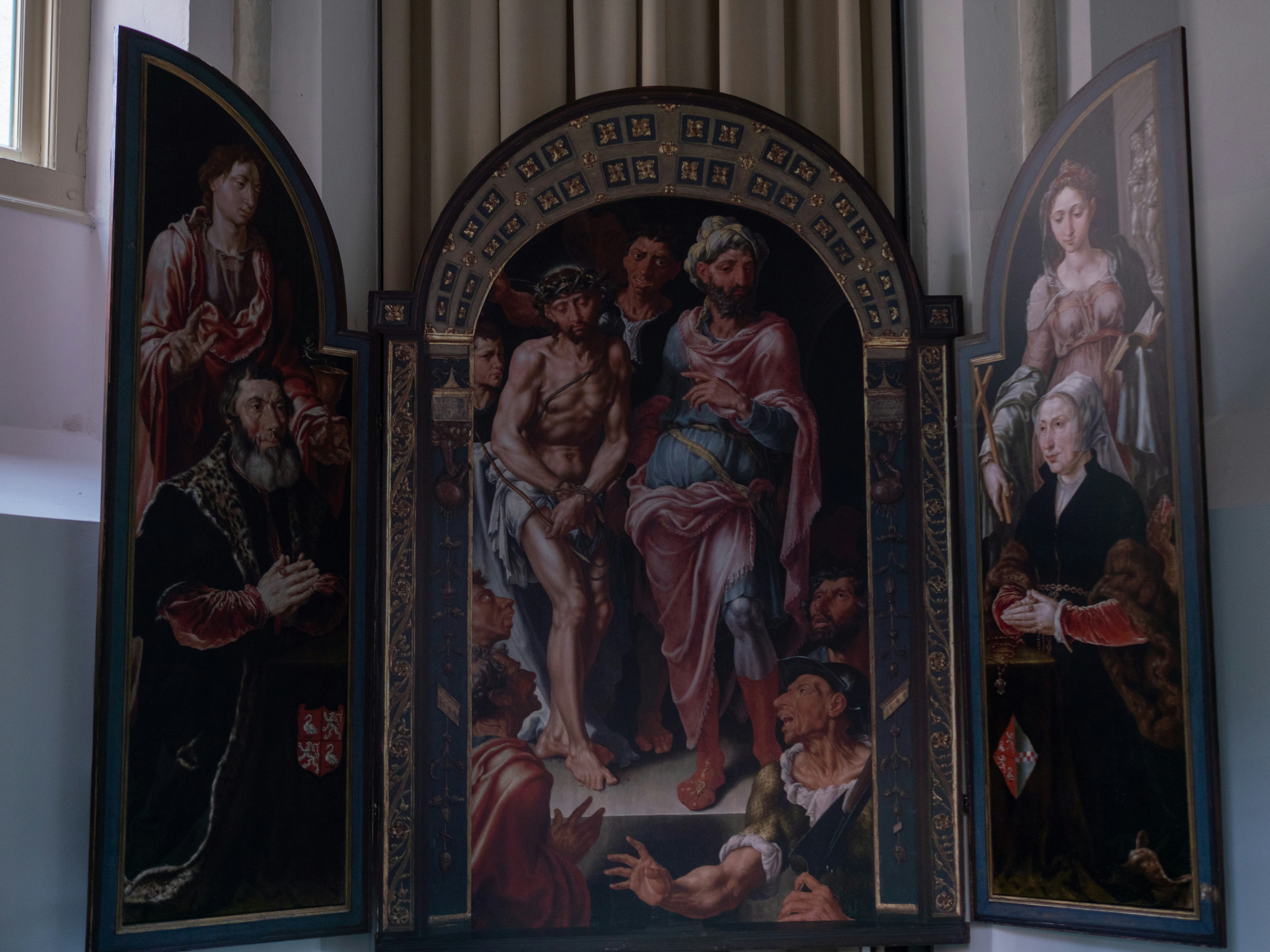 Intricately detailed triptych depicting biblical figures in a darkened chapel.