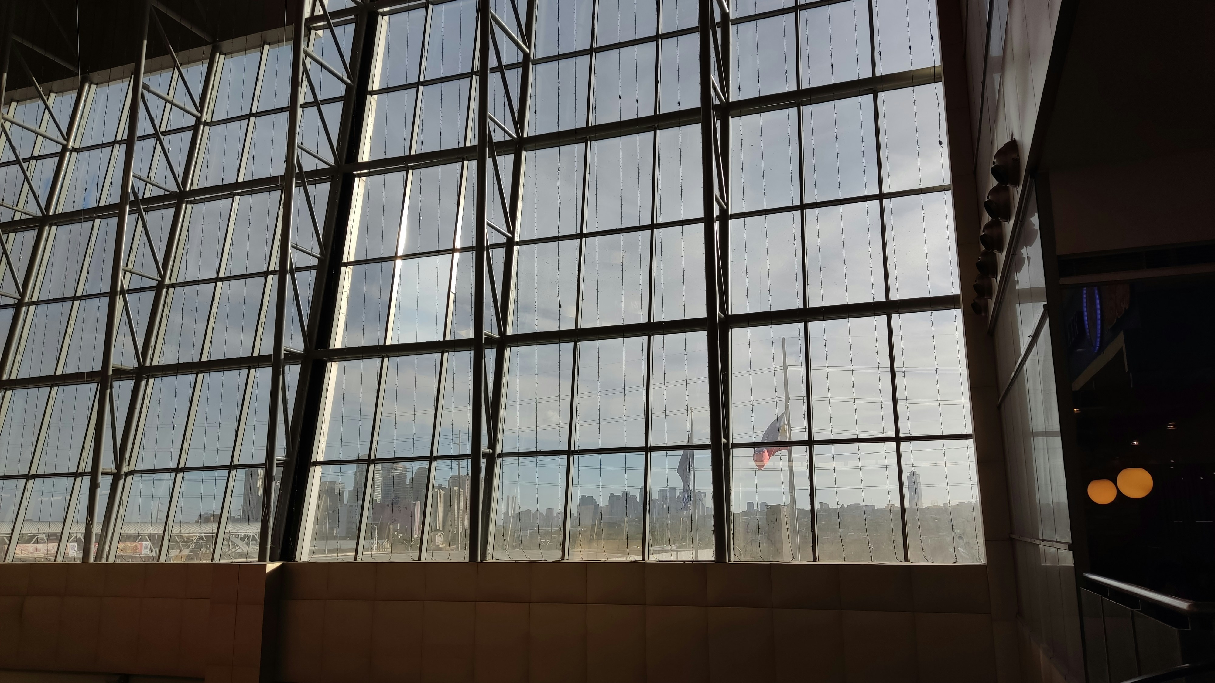 Large glass windows showcasing a city skyline with a distant flag fluttering. The interplay of light and reflections adds depth to the urban landscape.
