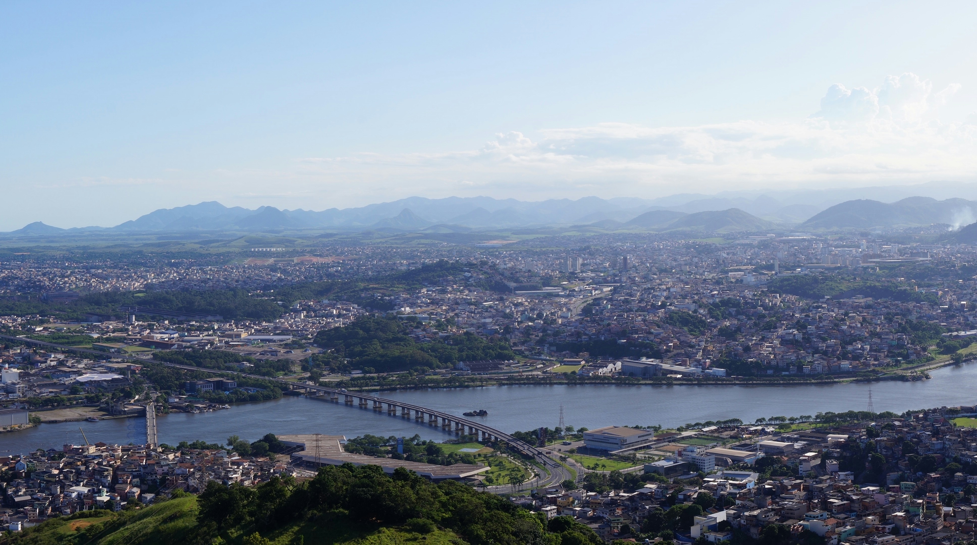 Expansive view of a cityscape with a river and bridge under a clear sky.