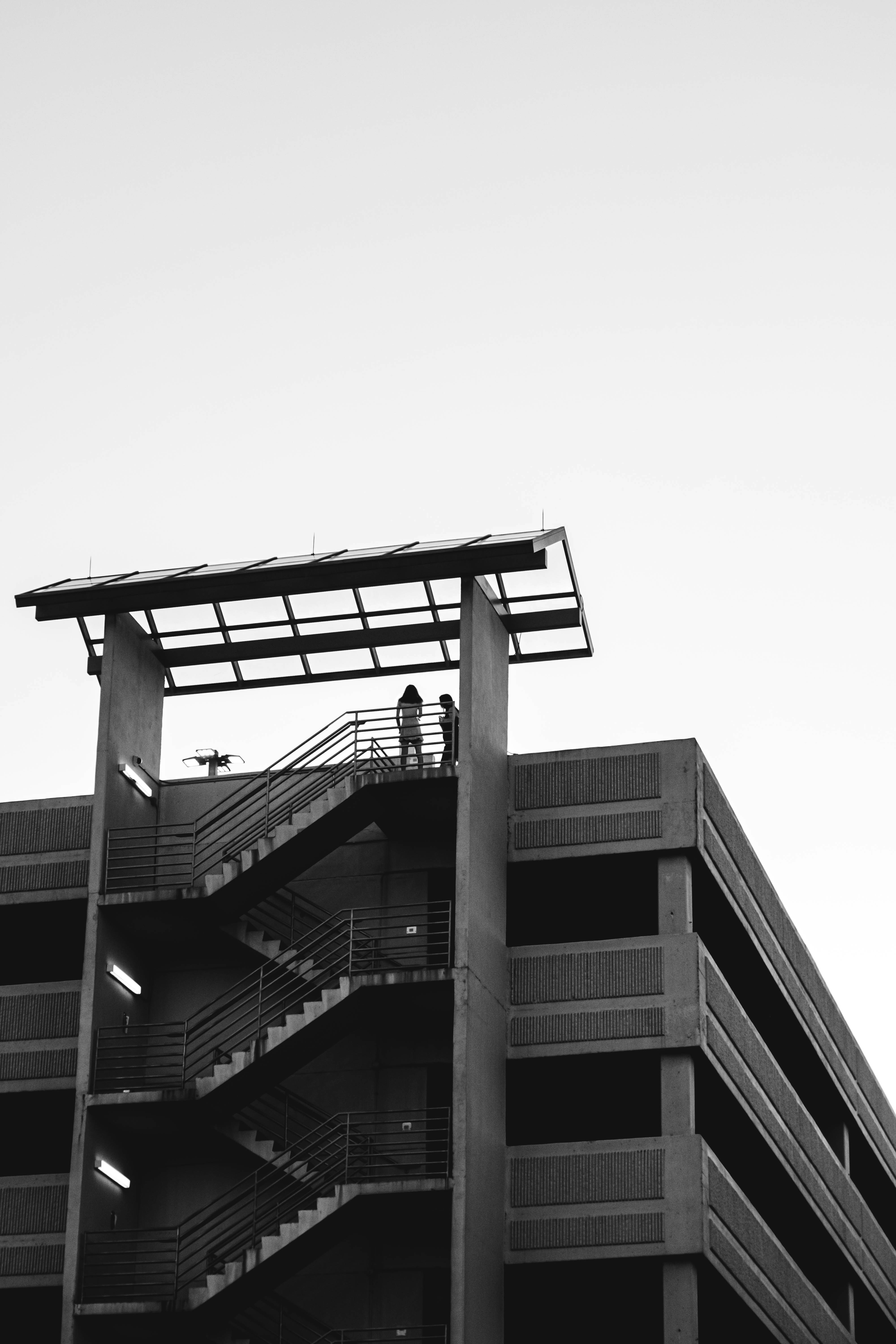 Two Silhouettes on the Edge of a Brutalist Rooftop Staircase