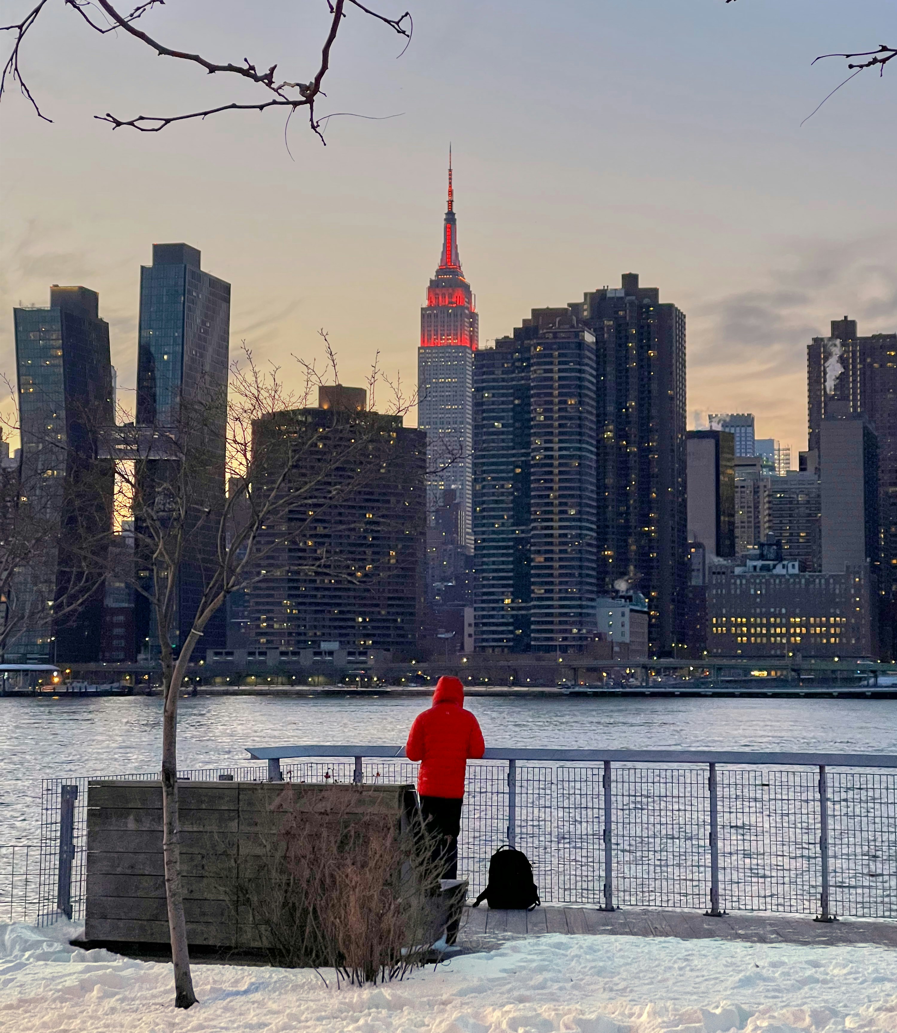Empire State Building illuminated in red against a snowy New York City skyline at dusk.