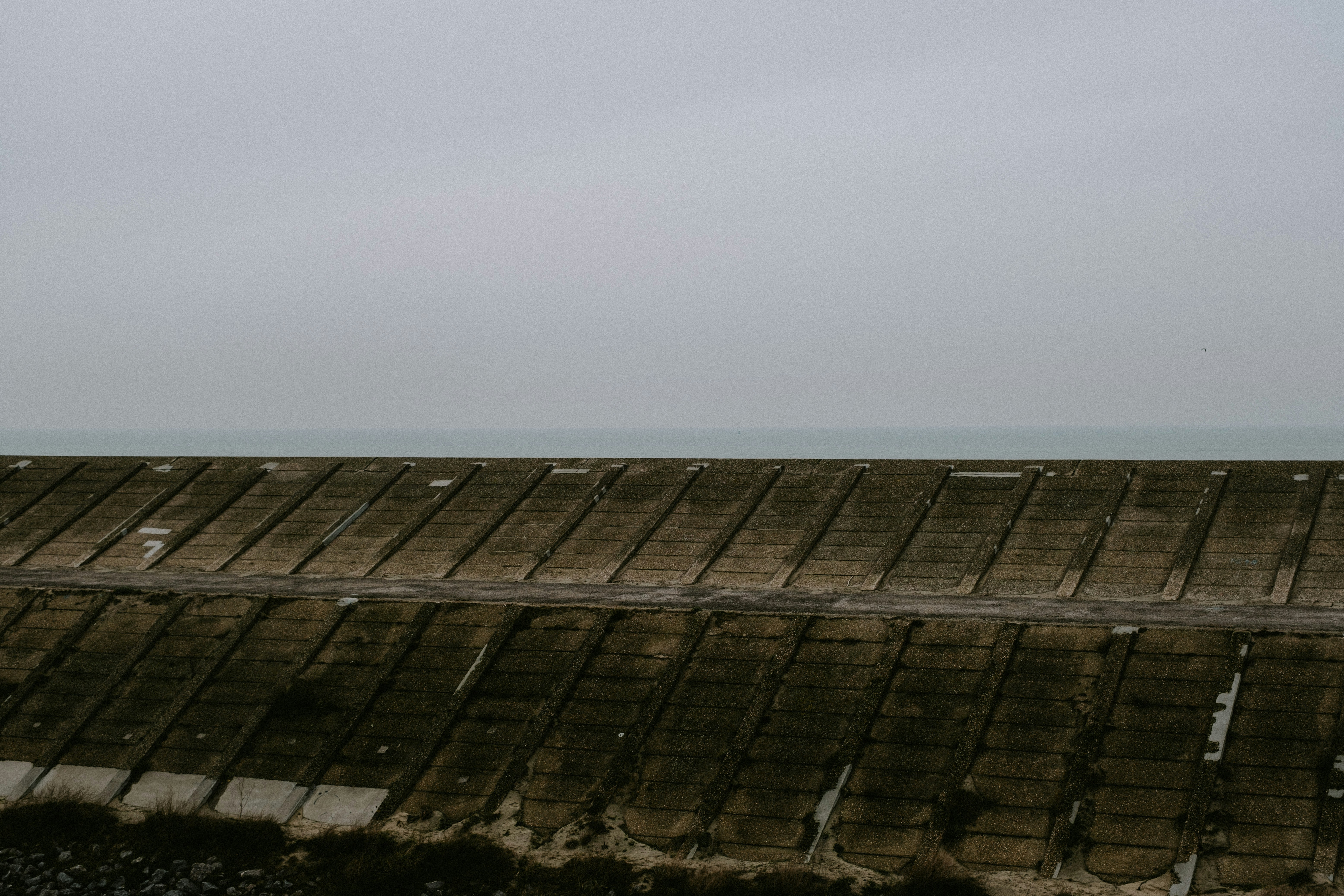 A textured concrete embankment meets a calm sea under a muted sky, illustrating the serene intersection of man-made structures and nature.
