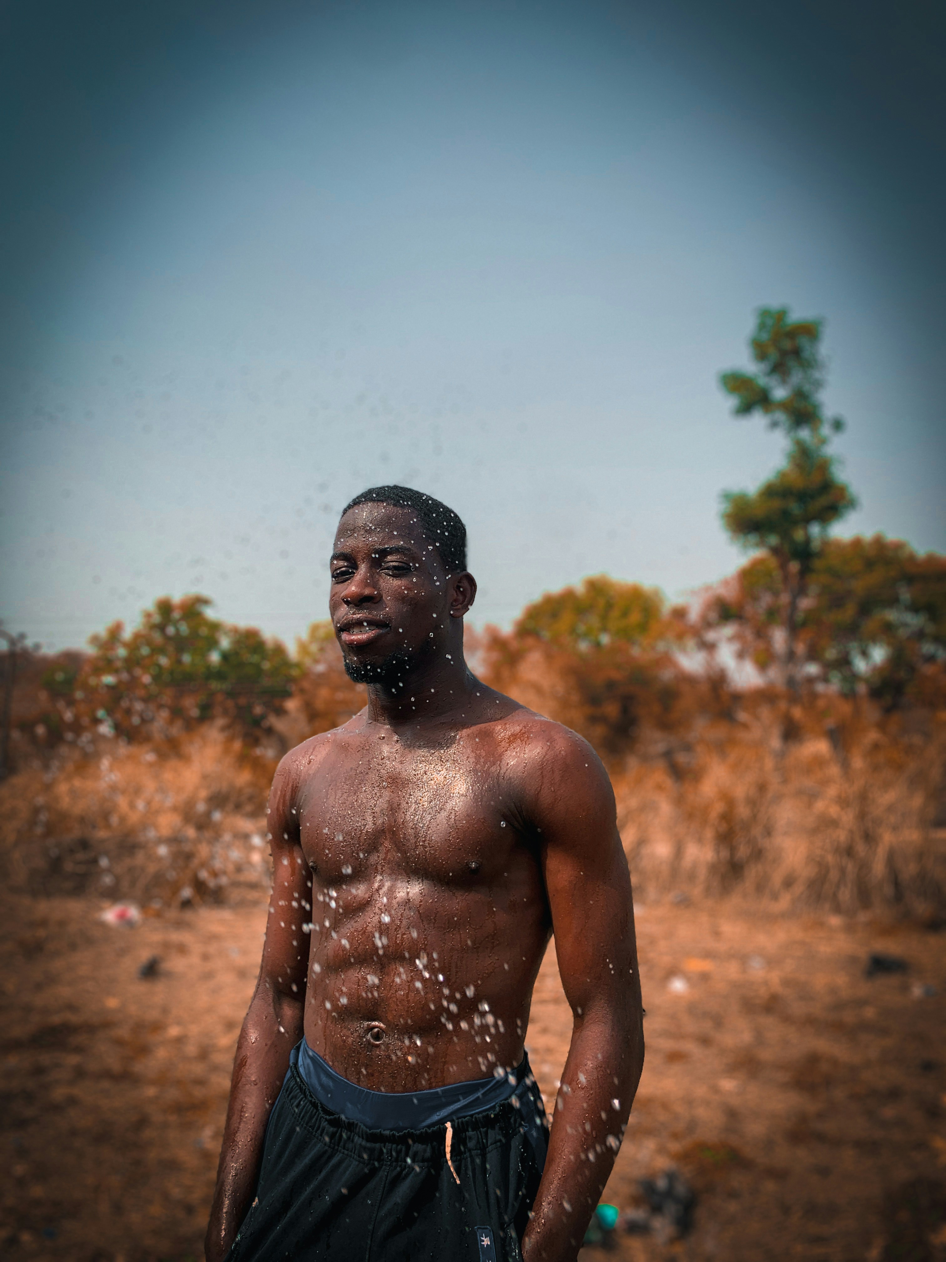 Man standing in a dry landscape, water droplets splashing around him, showcasing a moment of refreshment and vitality.