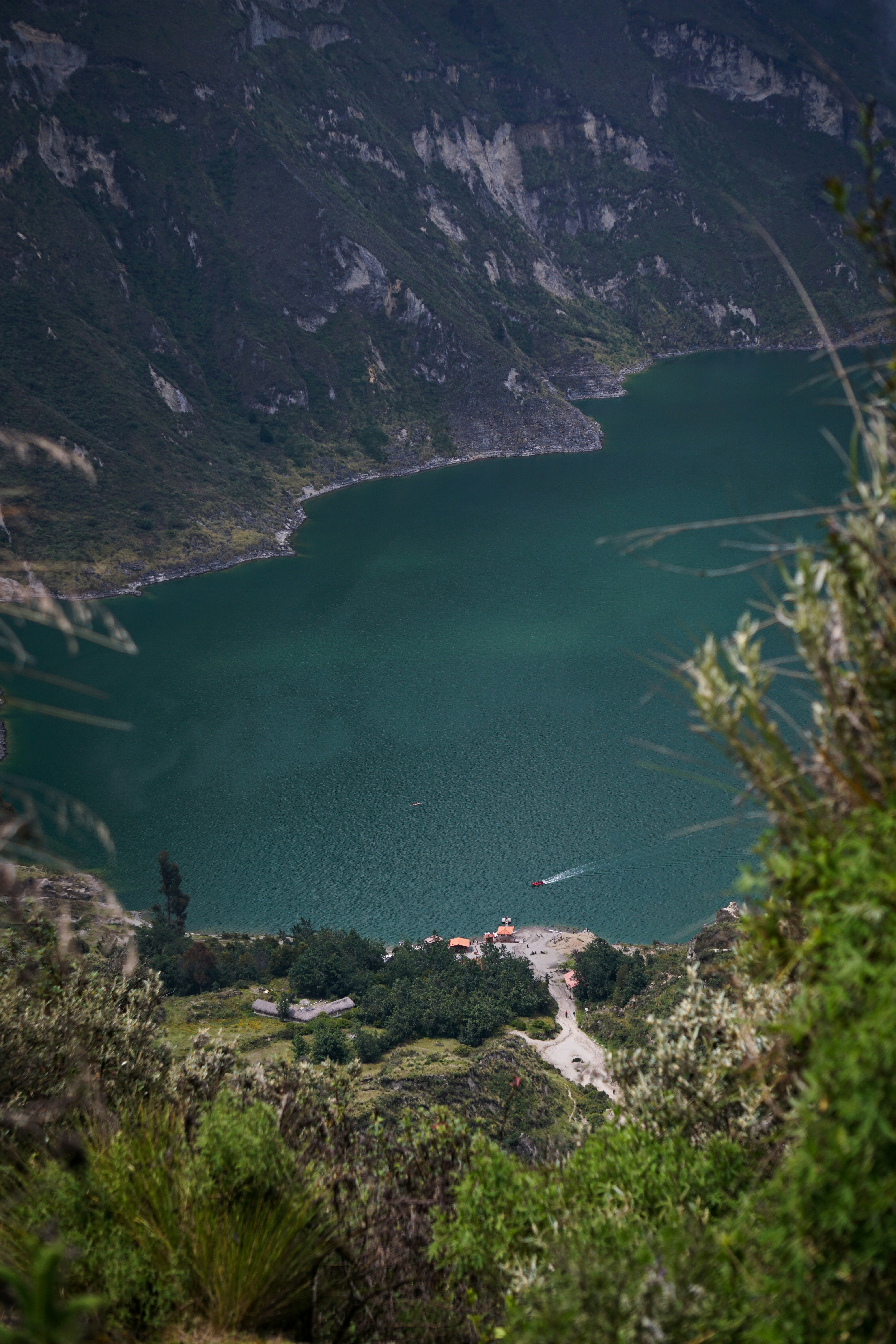 A tranquil lake nestled among rugged mountains, with a small boat gliding across the water's surface. Lush greenery frames the scene, enhancing its natural beauty.