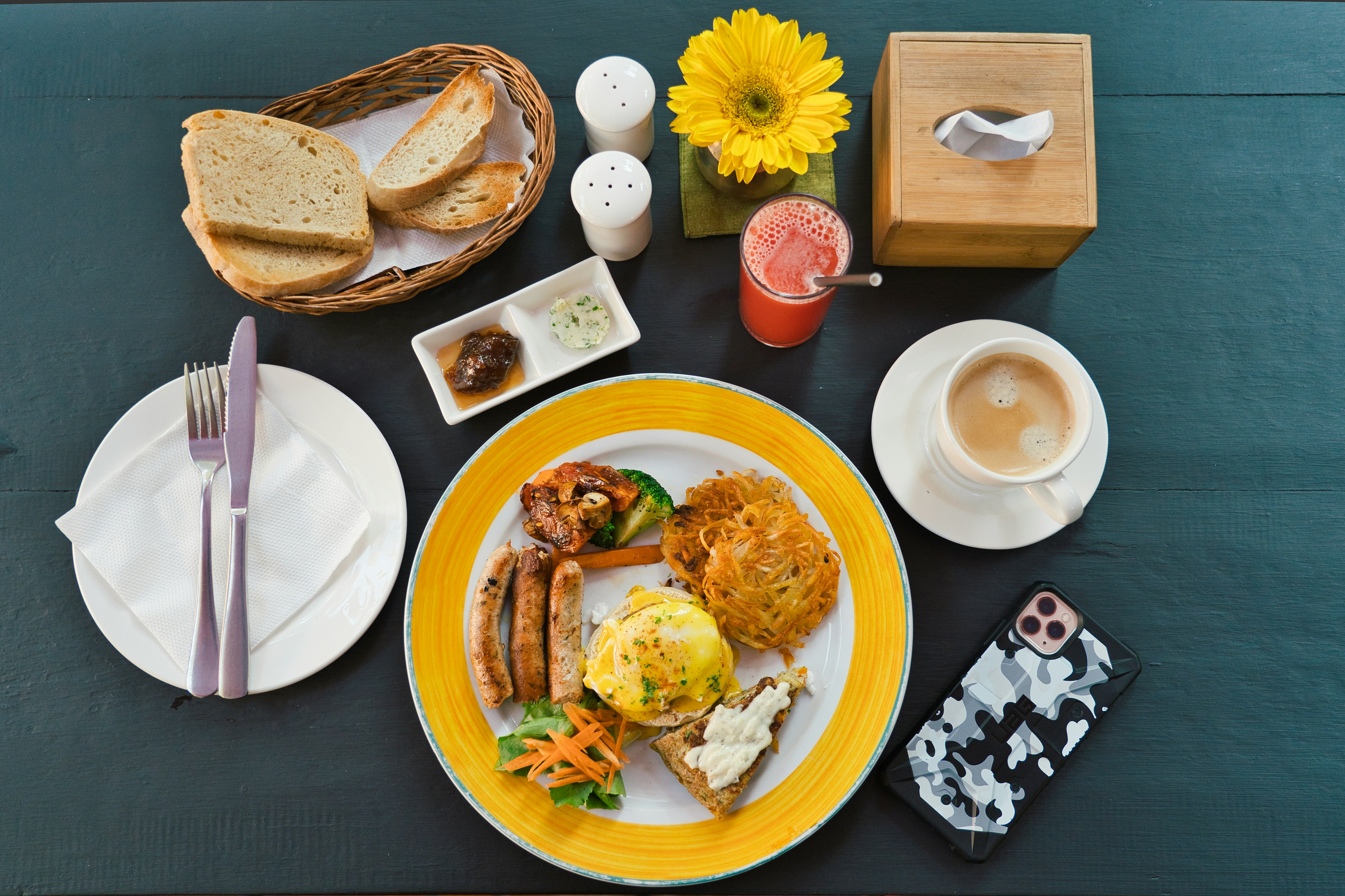 A vibrant breakfast spread featuring eggs, sausages, and toast arranged artfully on a round plate, complemented by a drink and a flower centerpiece.