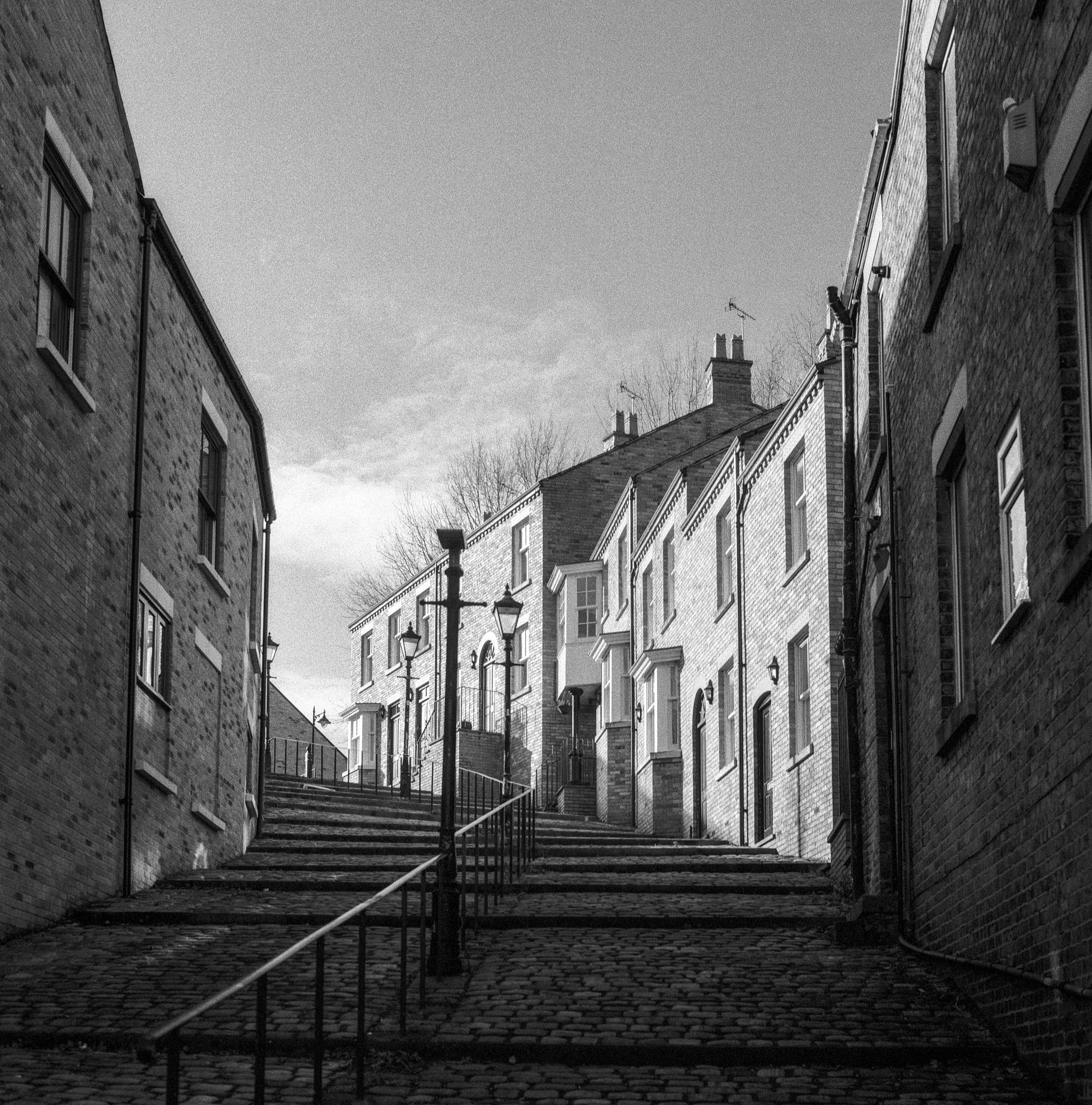 Black and white photograph of historic brick buildings lining a steep, cobbled street in Stockport, England.