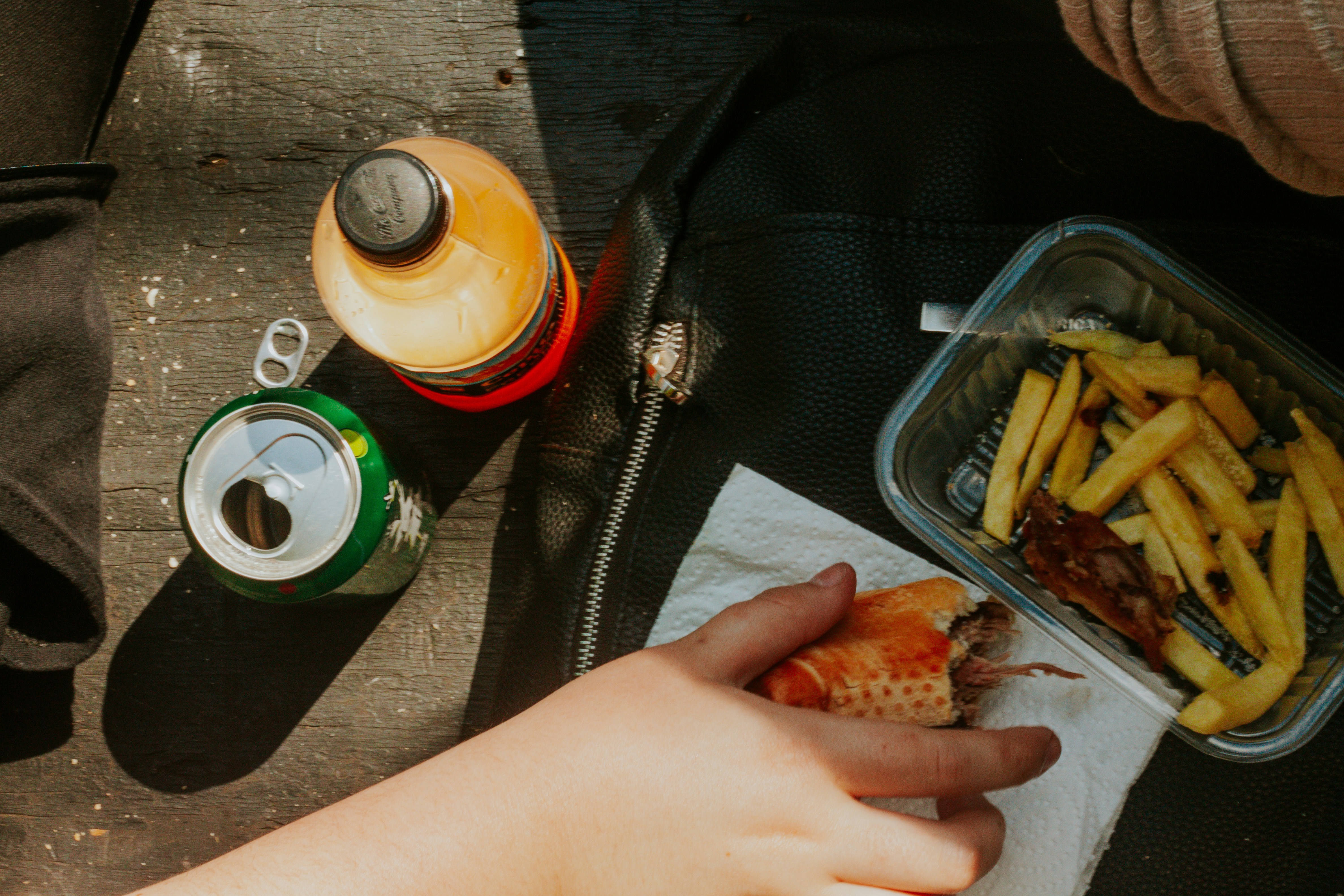 A hand reaches for a sandwich while a side of fries and beverages are arranged on a textured surface, highlighting a moment of casual dining.