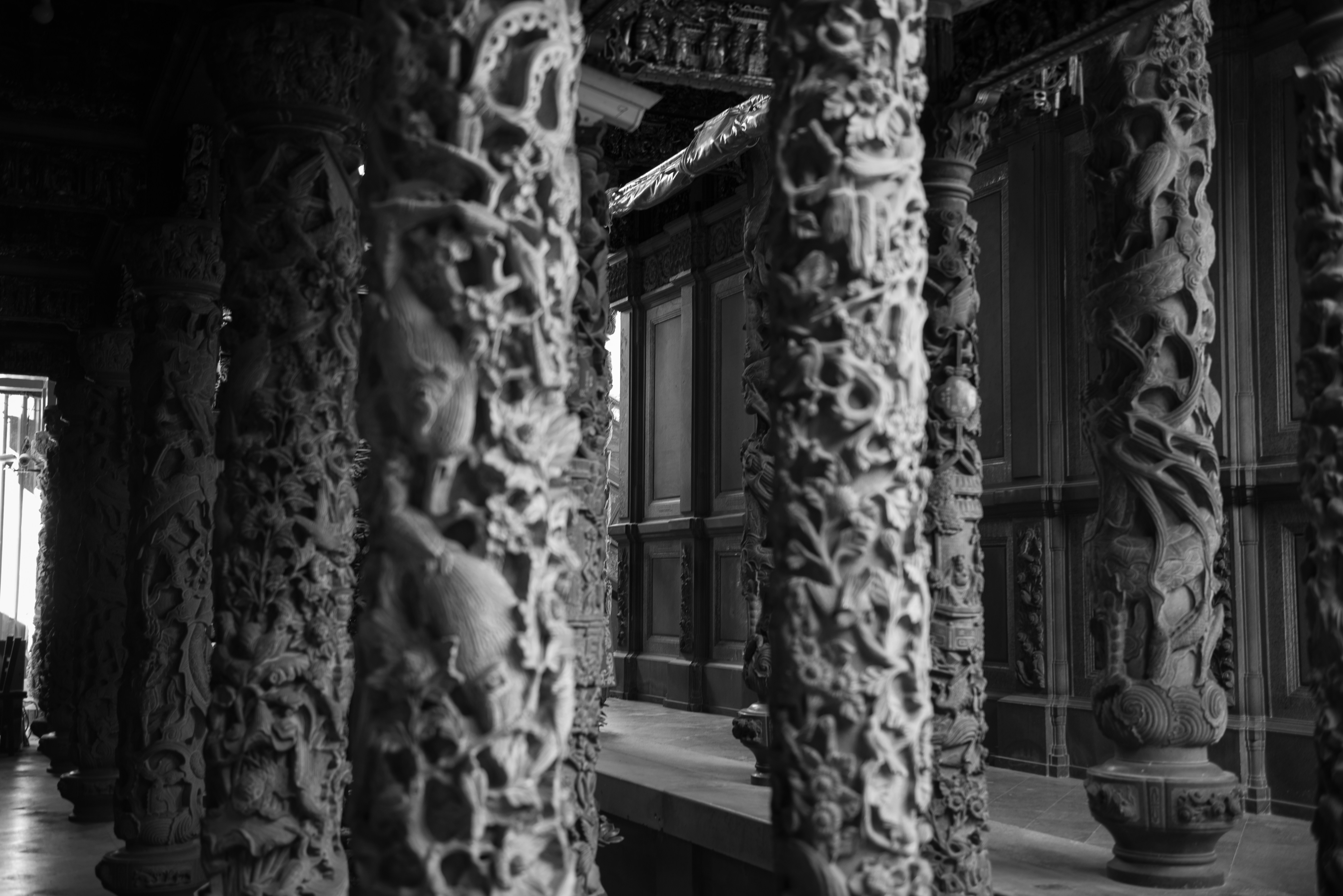 Ornately carved pillars line a dimly lit corridor, showcasing detailed artistry and craftsmanship in monochrome tones.