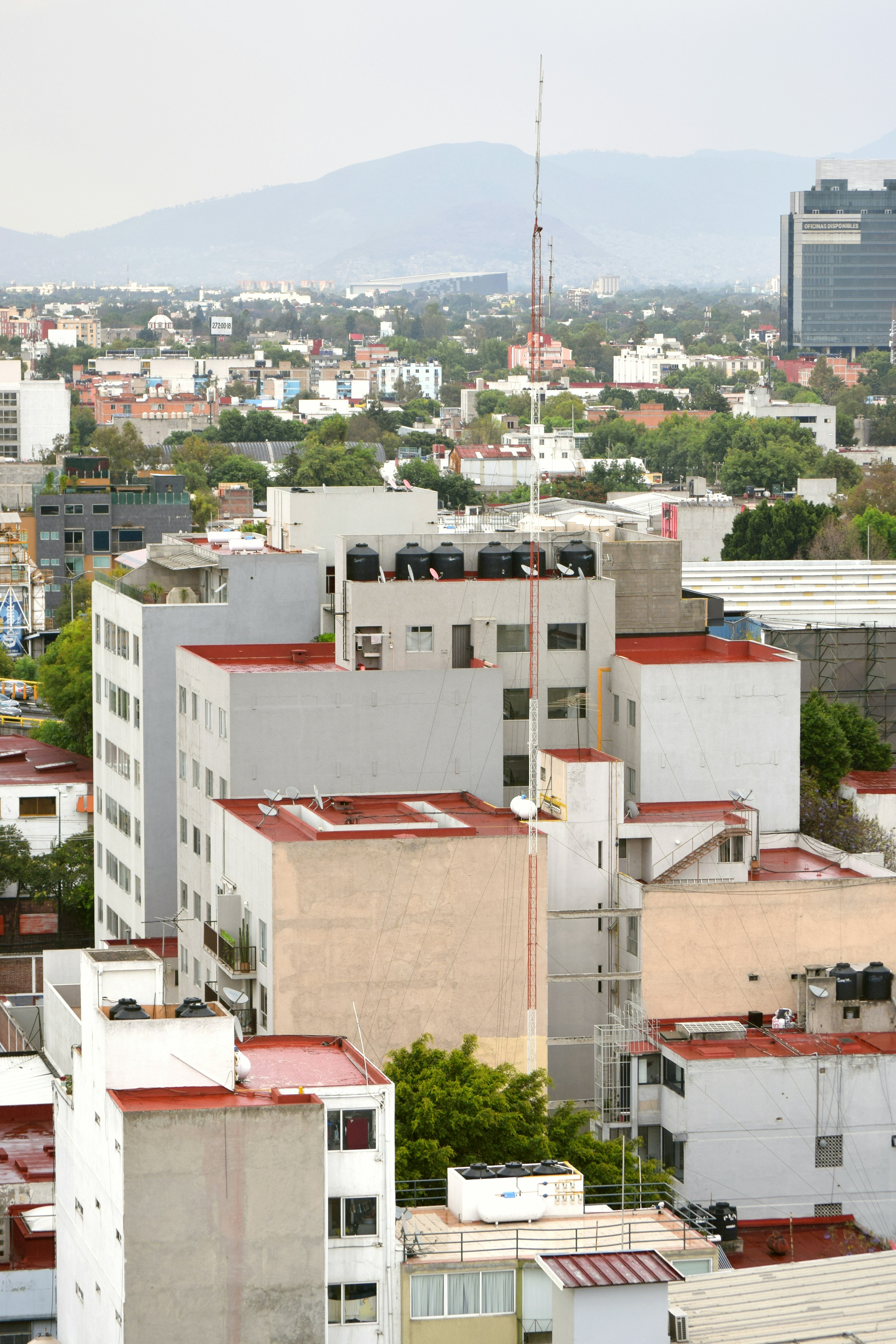 Aerial view of a vibrant urban landscape featuring a mix of residential buildings and greenery, showcasing the intricate layout of the city. The rooftops display a variety of colors and textures.