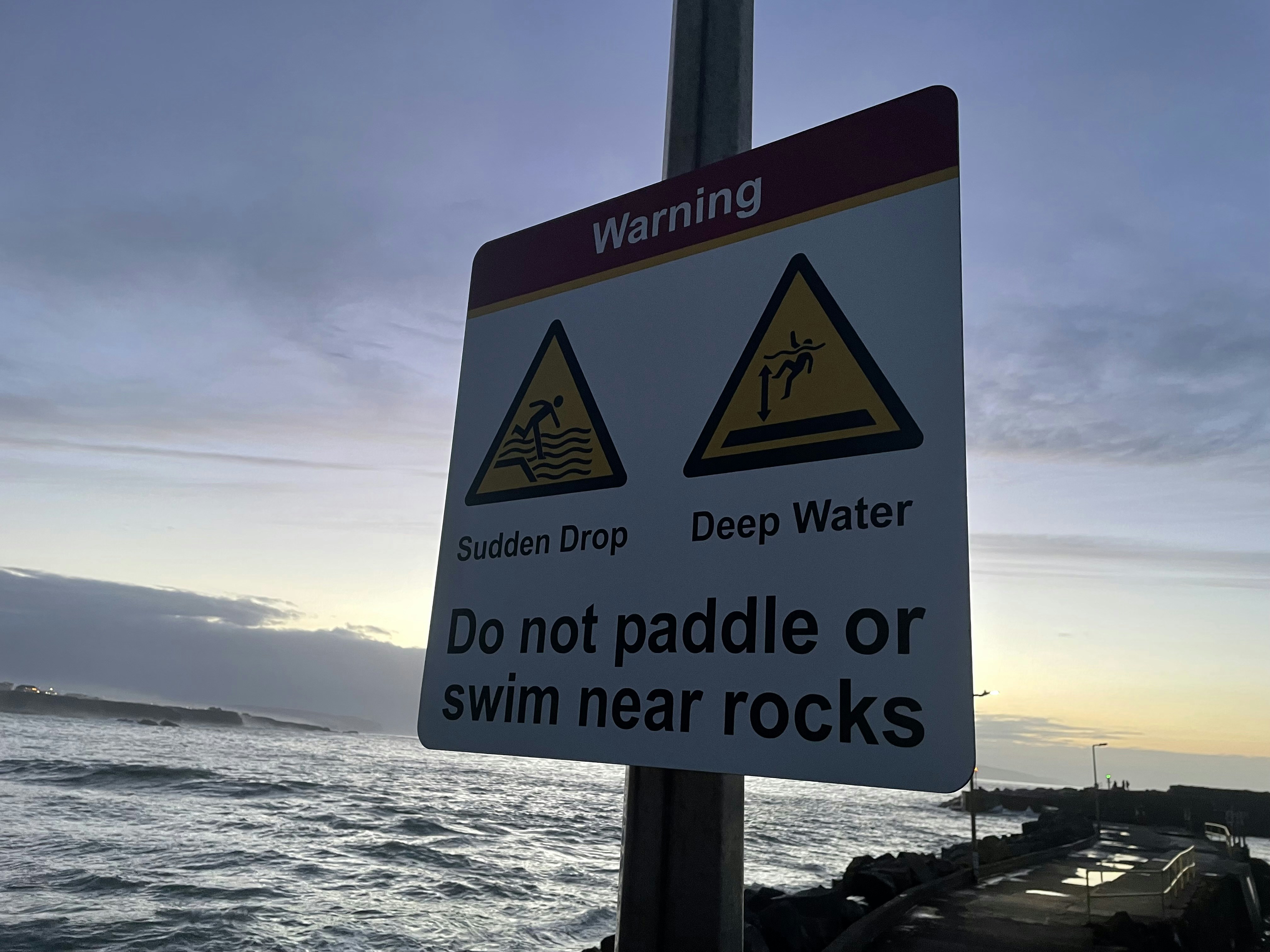 A warning sign on a pole near the ocean photo – Free Grey Image on Unsplash