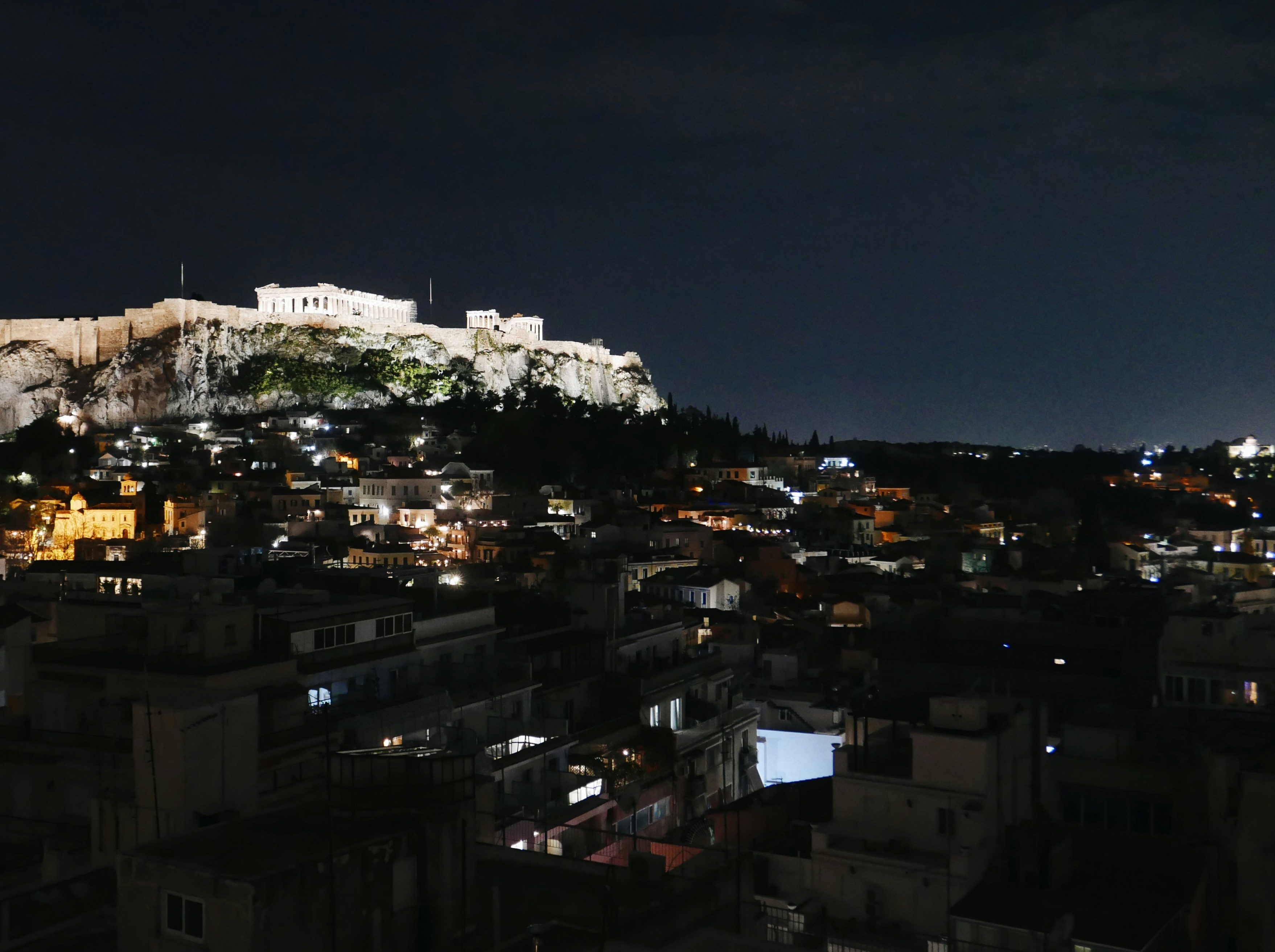 Acropolis of Athens illuminated against a dark sky, overlooking the cityscape filled with twinkling lights.