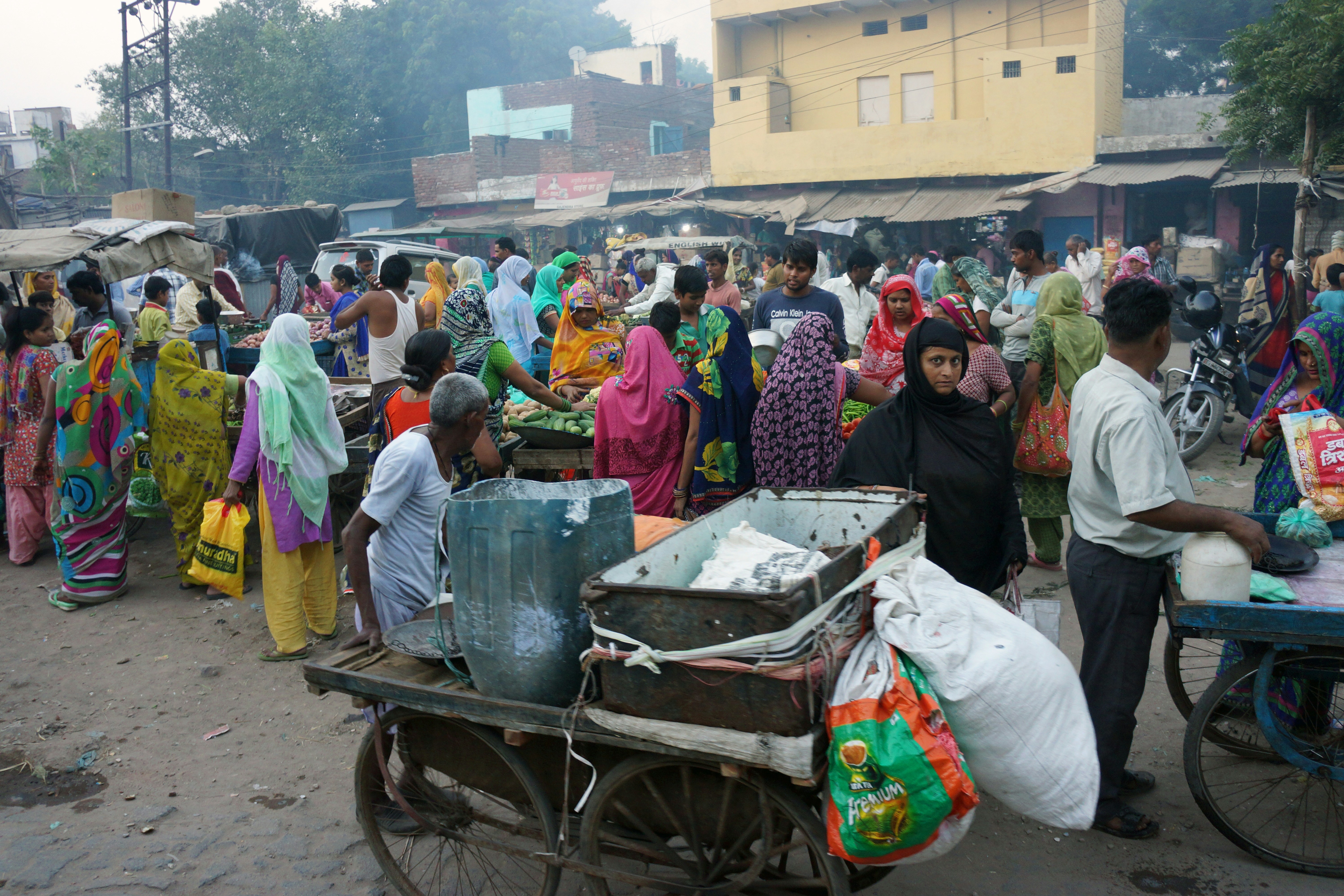 Bustling street market with vendors and shoppers in colorful attire around carts and stalls.