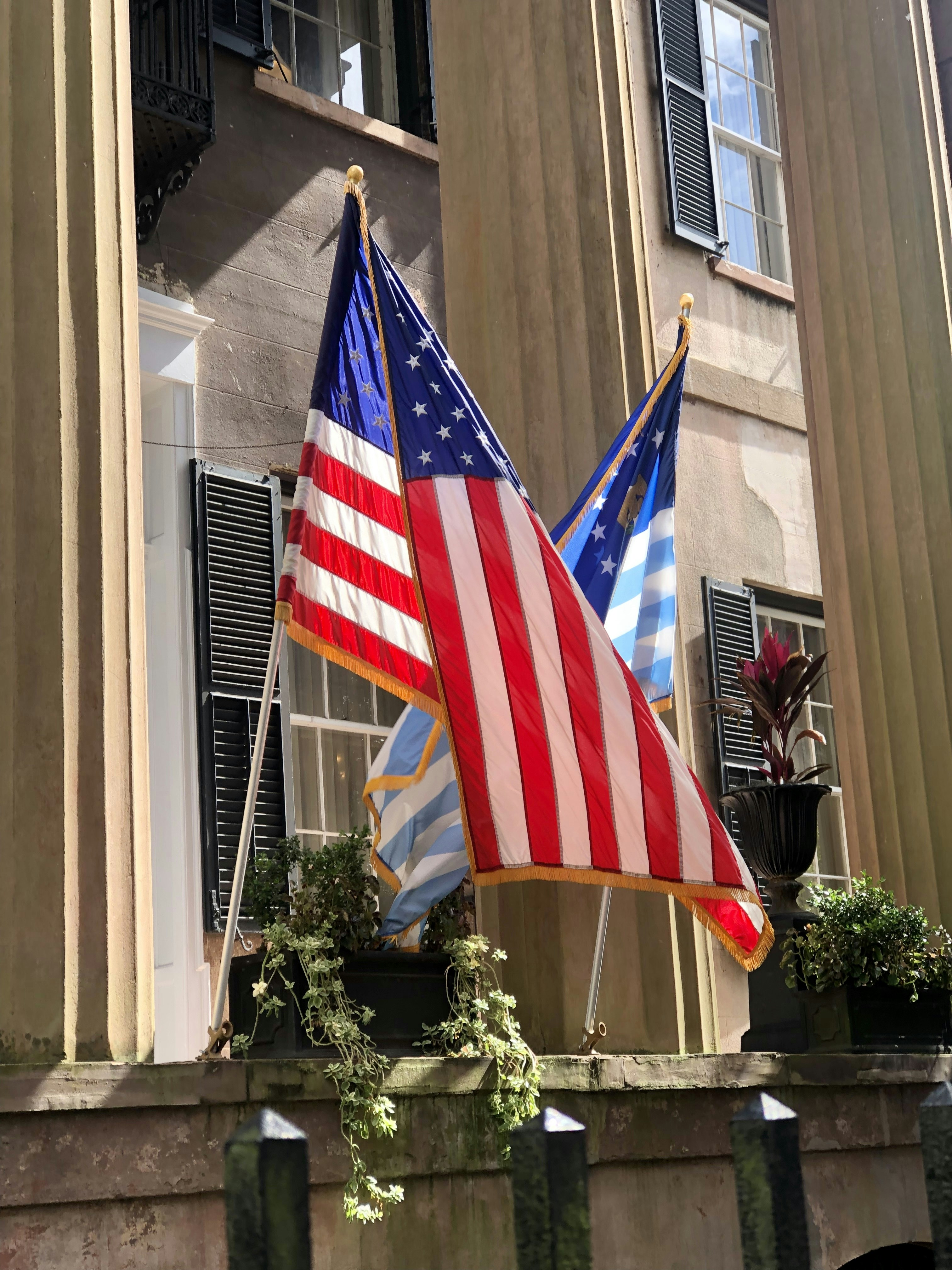 Sunlit Banner on a Stone Veranda: Flags Framing a Classic Facade