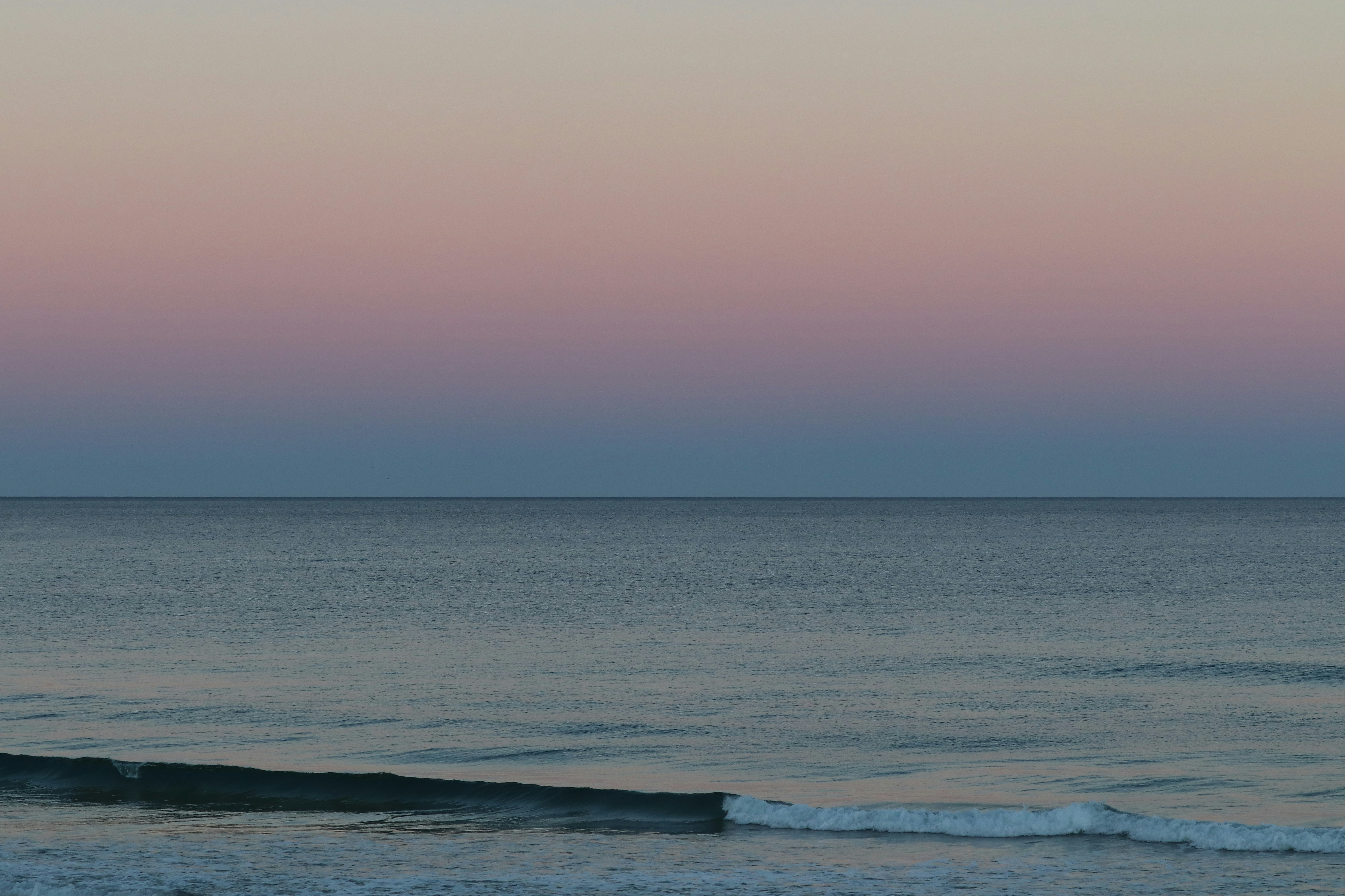 Gentle waves kiss the shore under a pastel sky transitioning from soft pink to serene blue.
