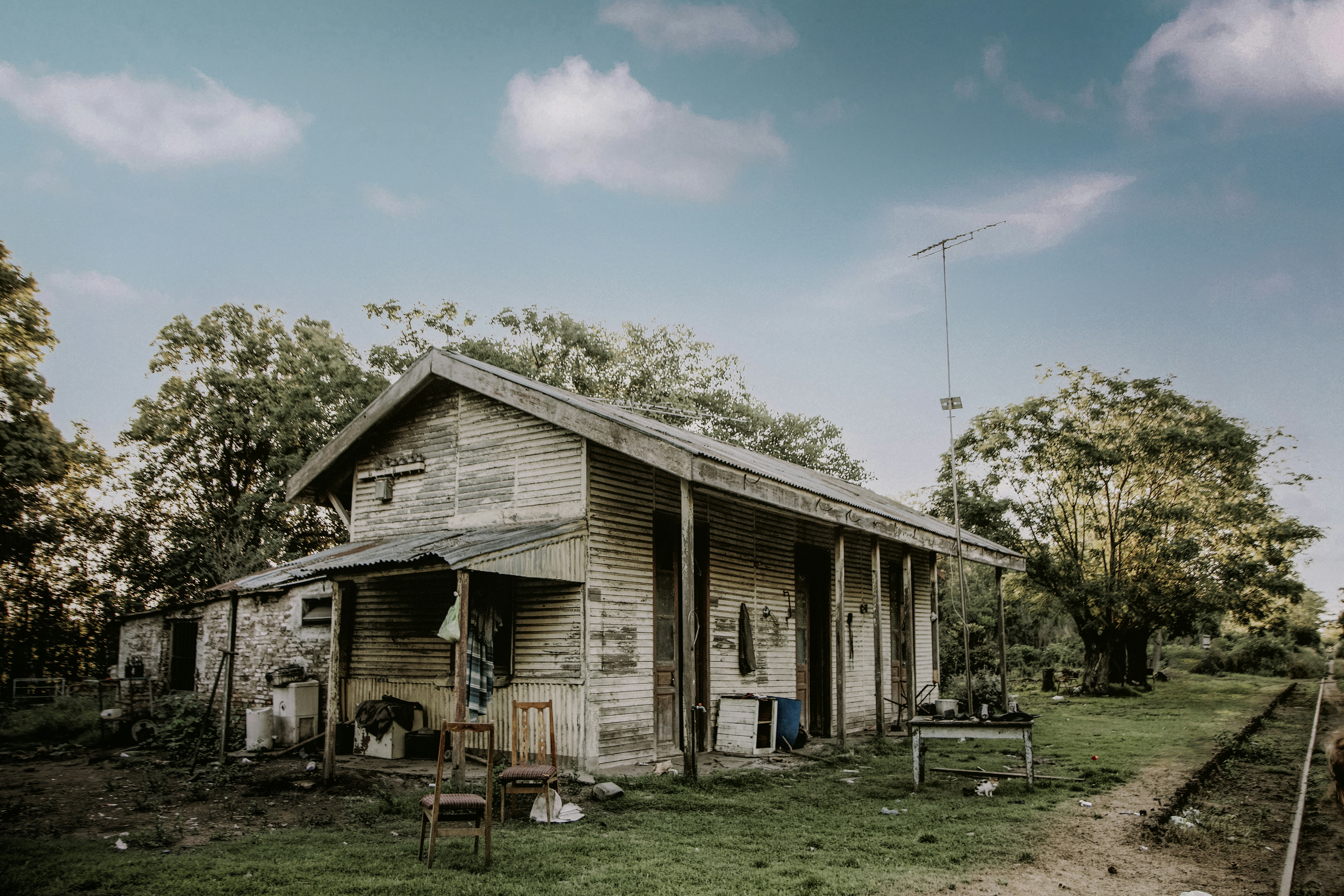 A weathered wooden house stands solitary amidst overgrown grass and trees, evoking a sense of nostalgia and forgotten stories.