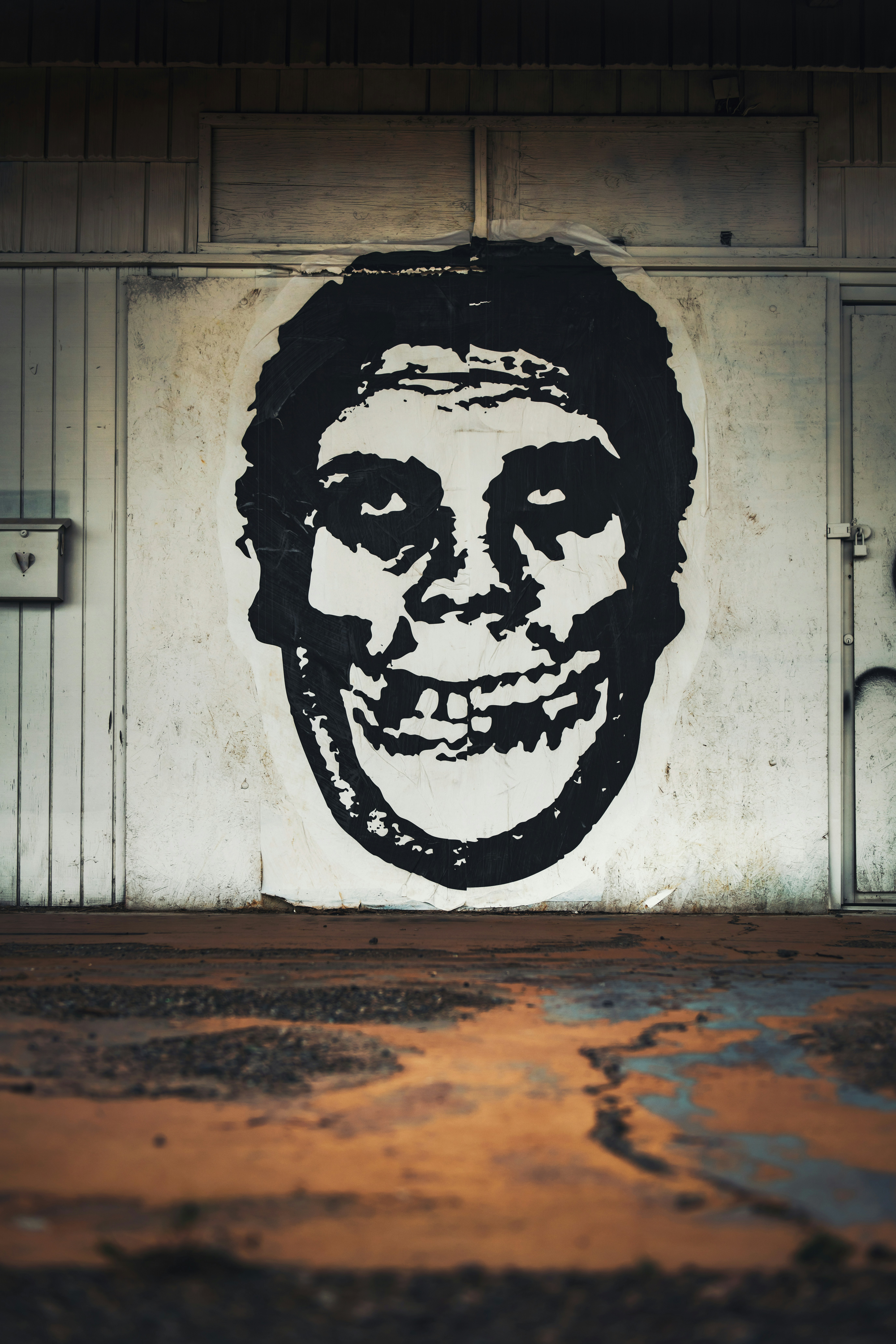 Bold black-and-white mural depicting a stylized face on a weathered wooden surface.