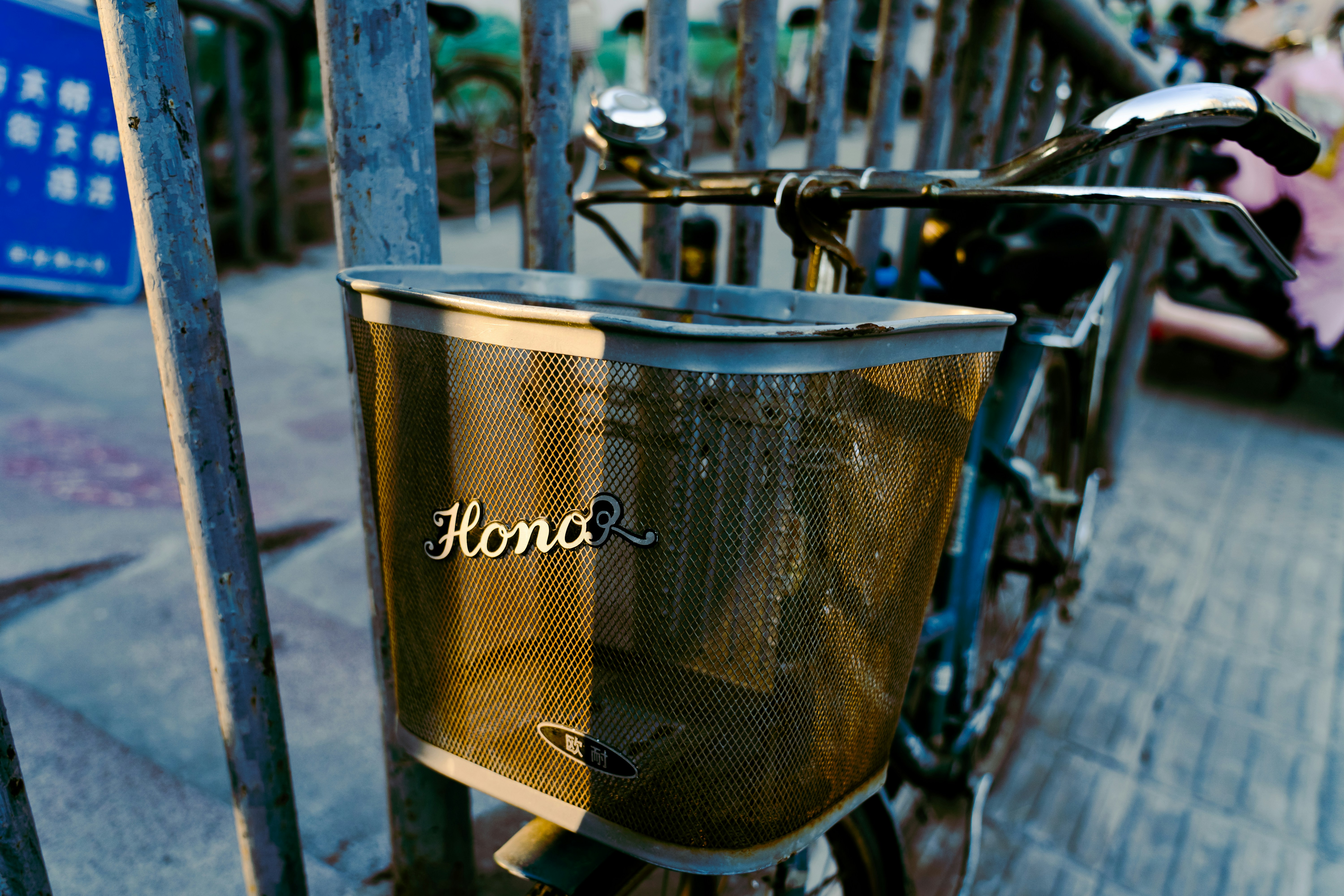 Close-up of a bicycle's metallic basket reflecting sunlight, showcasing intricate mesh details against a blurred urban backdrop.