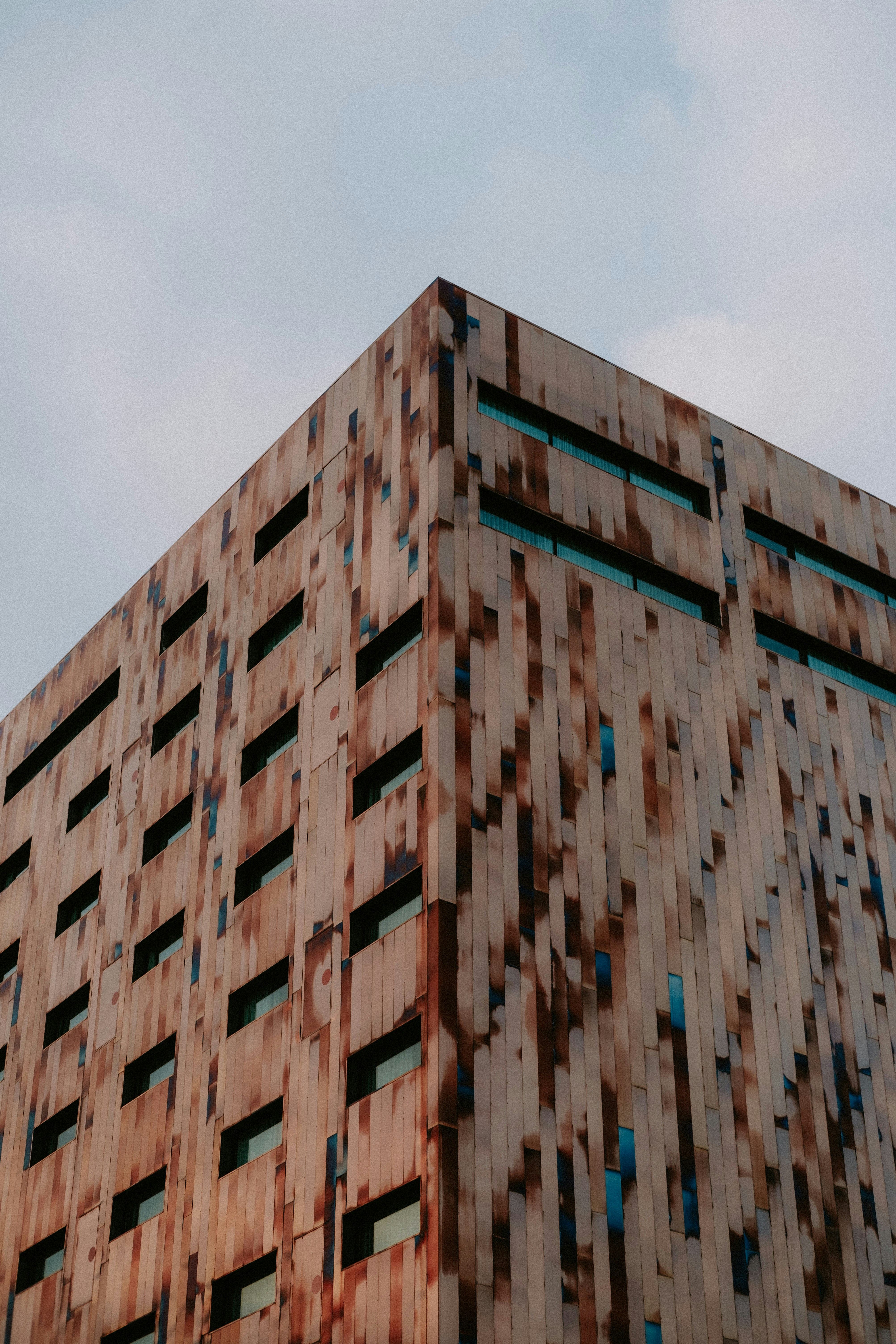 Abstract architectural detail of a building's facade, showcasing a blend of wood-like textures and vibrant colors. The interplay of light and shadow enhances its visual complexity.