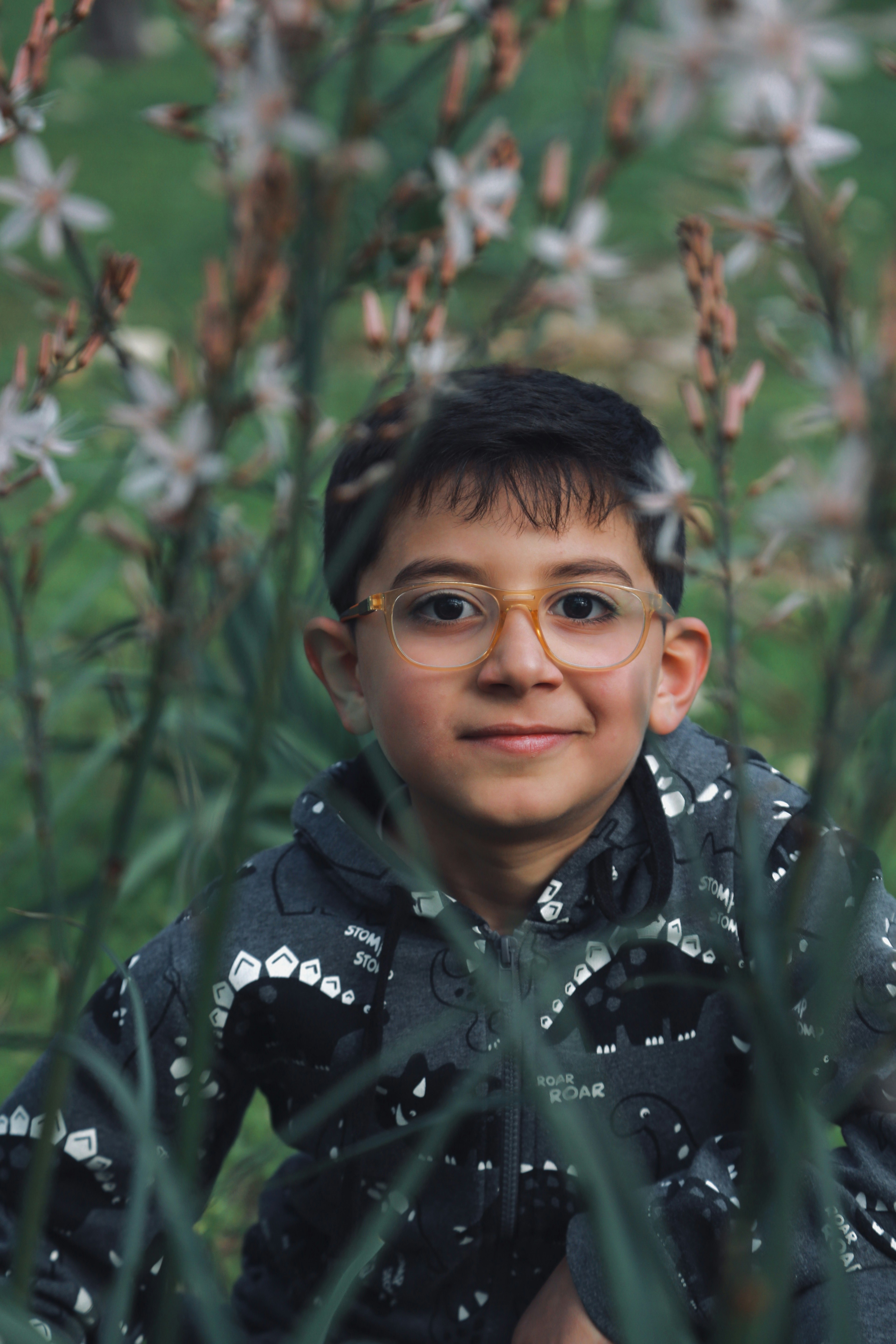 Child in glasses smiling through tall wildflowers in a garden.