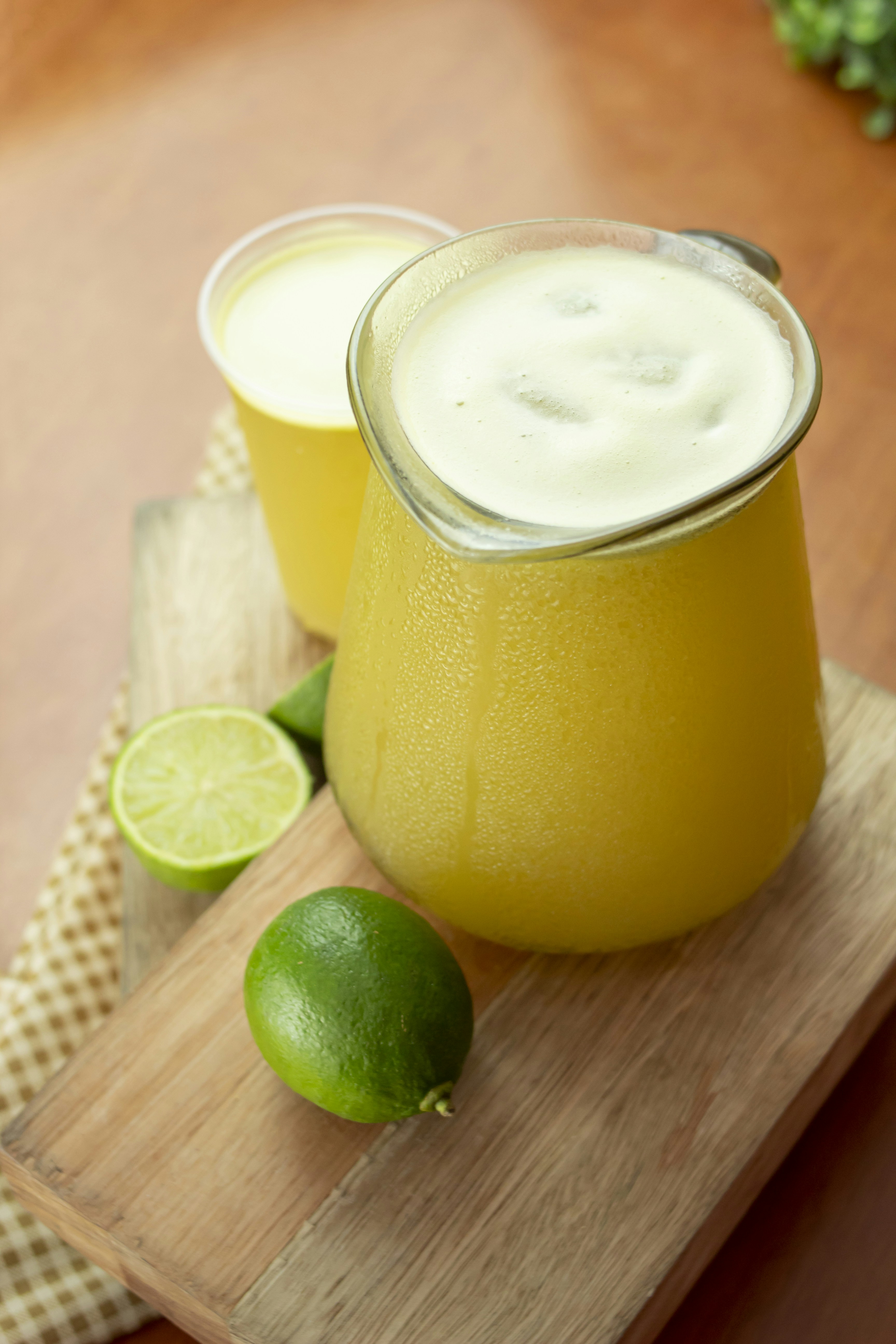 A pitcher of refreshing lime drink accompanied by a glass and fresh limes on a wooden surface.