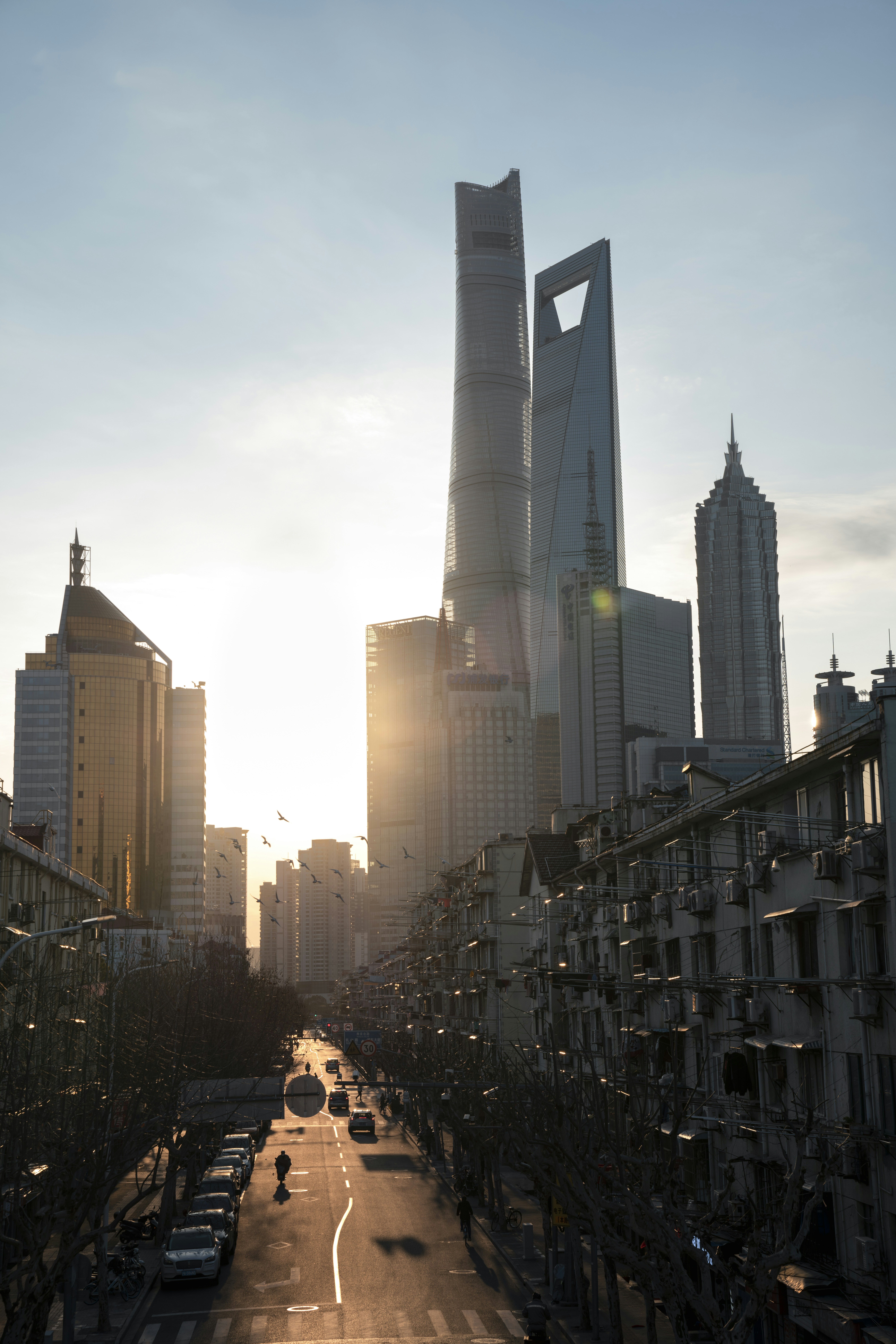 Skyscrapers of Shanghai silhouetted against a sunset, with bustling streets below. The scene captures the dynamic contrast between modern architecture and urban life.