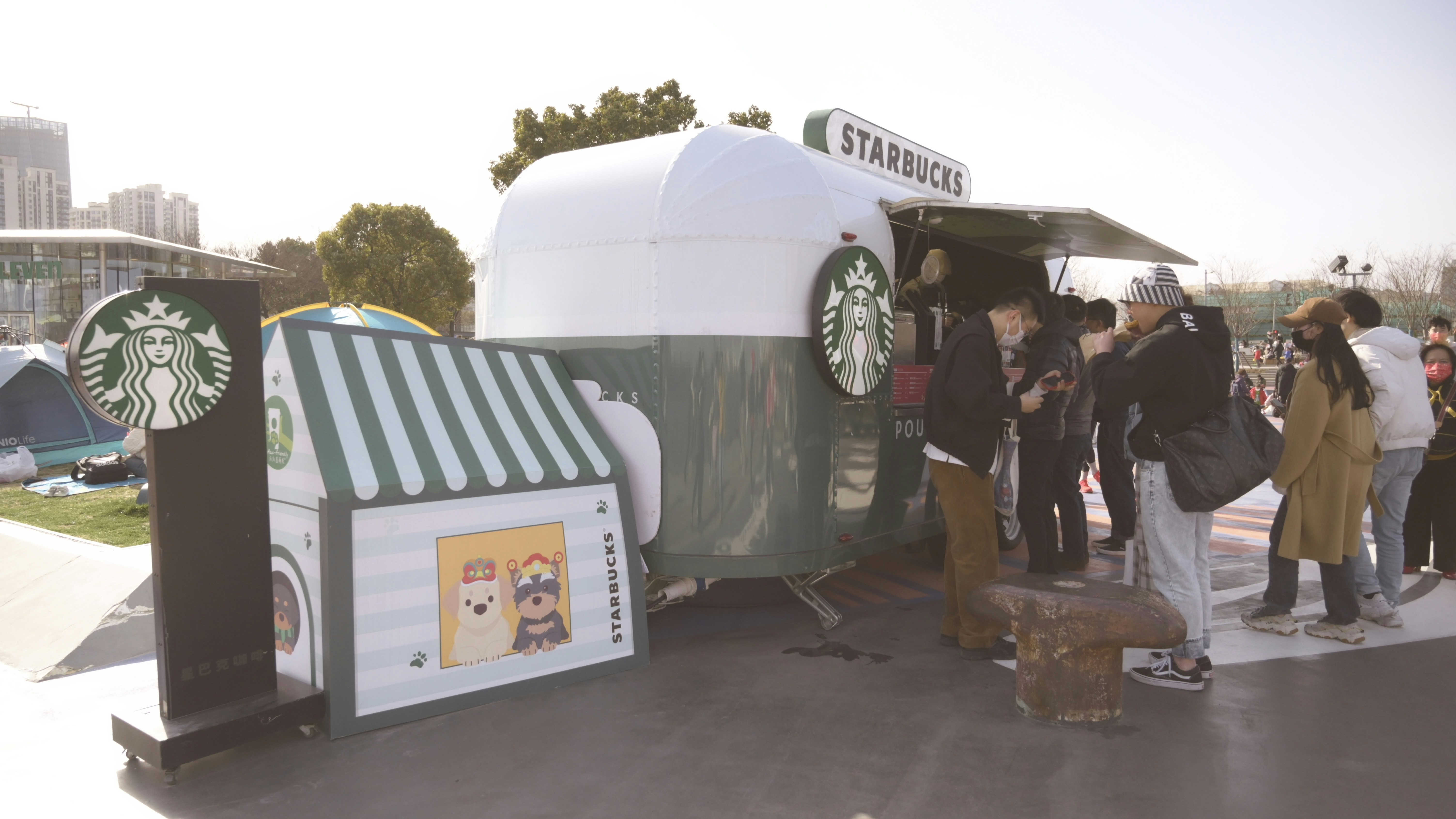 A vibrant mobile Starbucks coffee cart surrounded by eager customers, showcasing a playful design with a whimsical character illustration. 