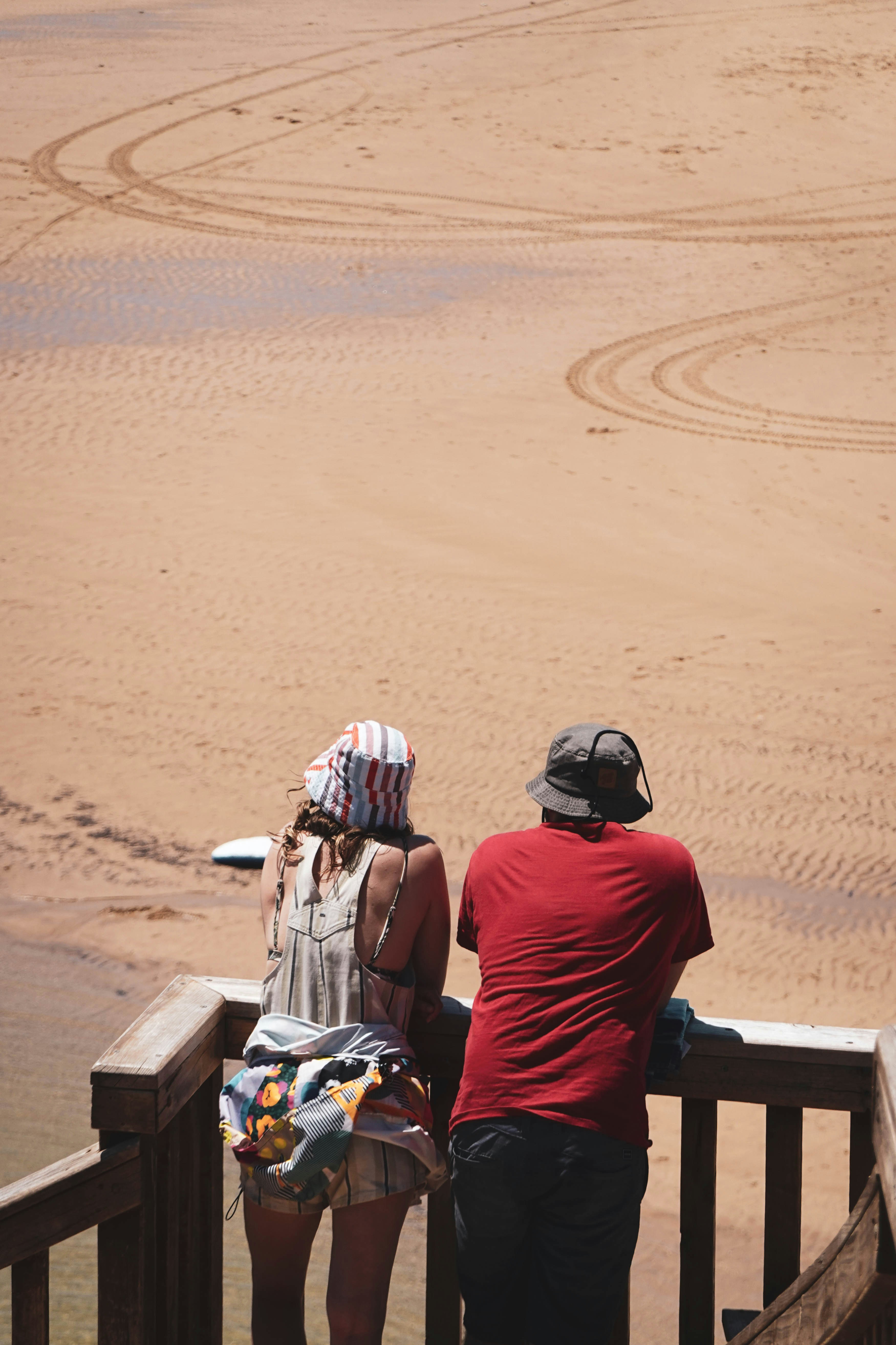 Two Silhouettes at a Wooden Railing Over a Wind-Sculpted Sand Landscape