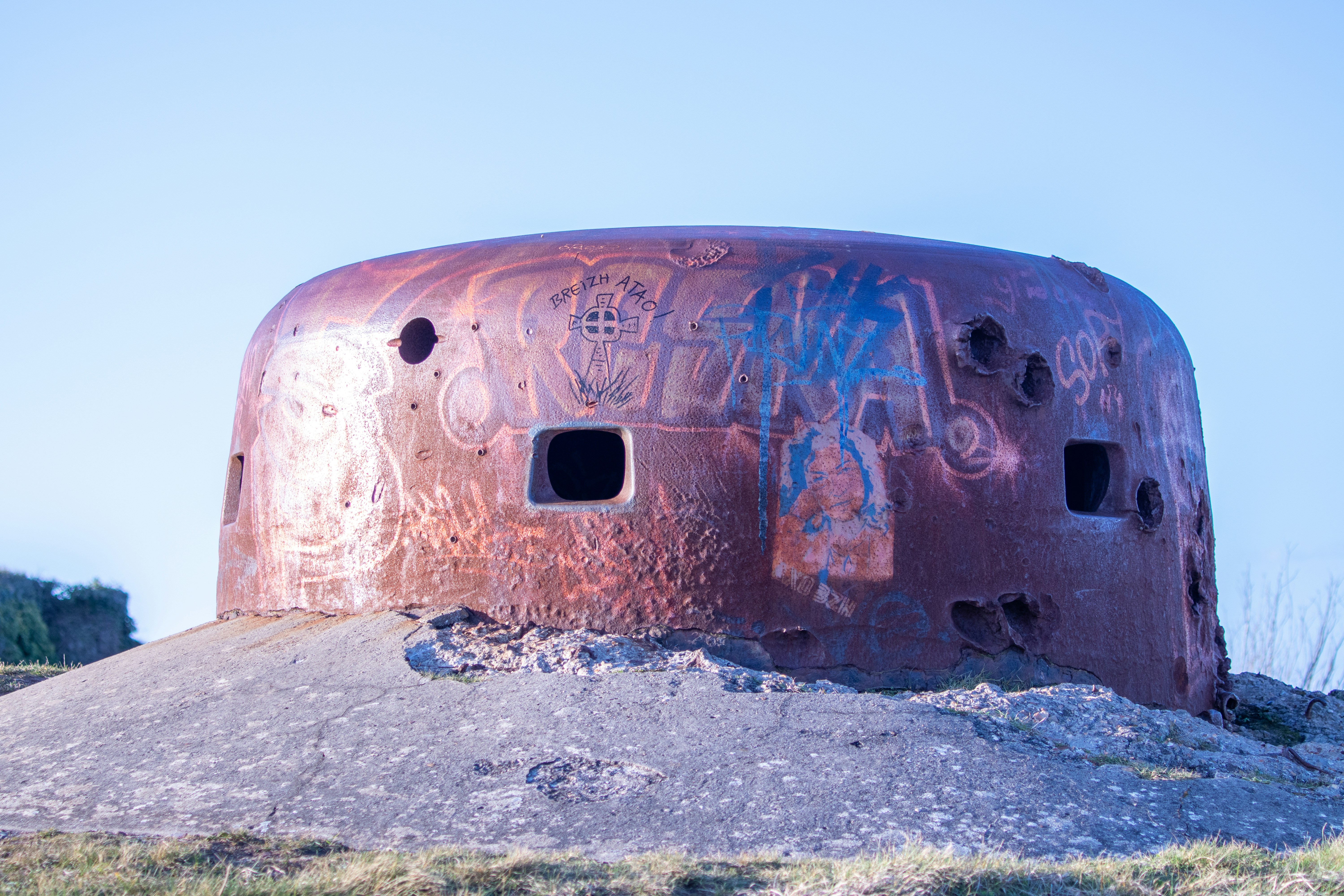 Rusty coastal bunker adorned with graffiti, standing resilient against the elements. A testament to past conflicts and modern artistry.